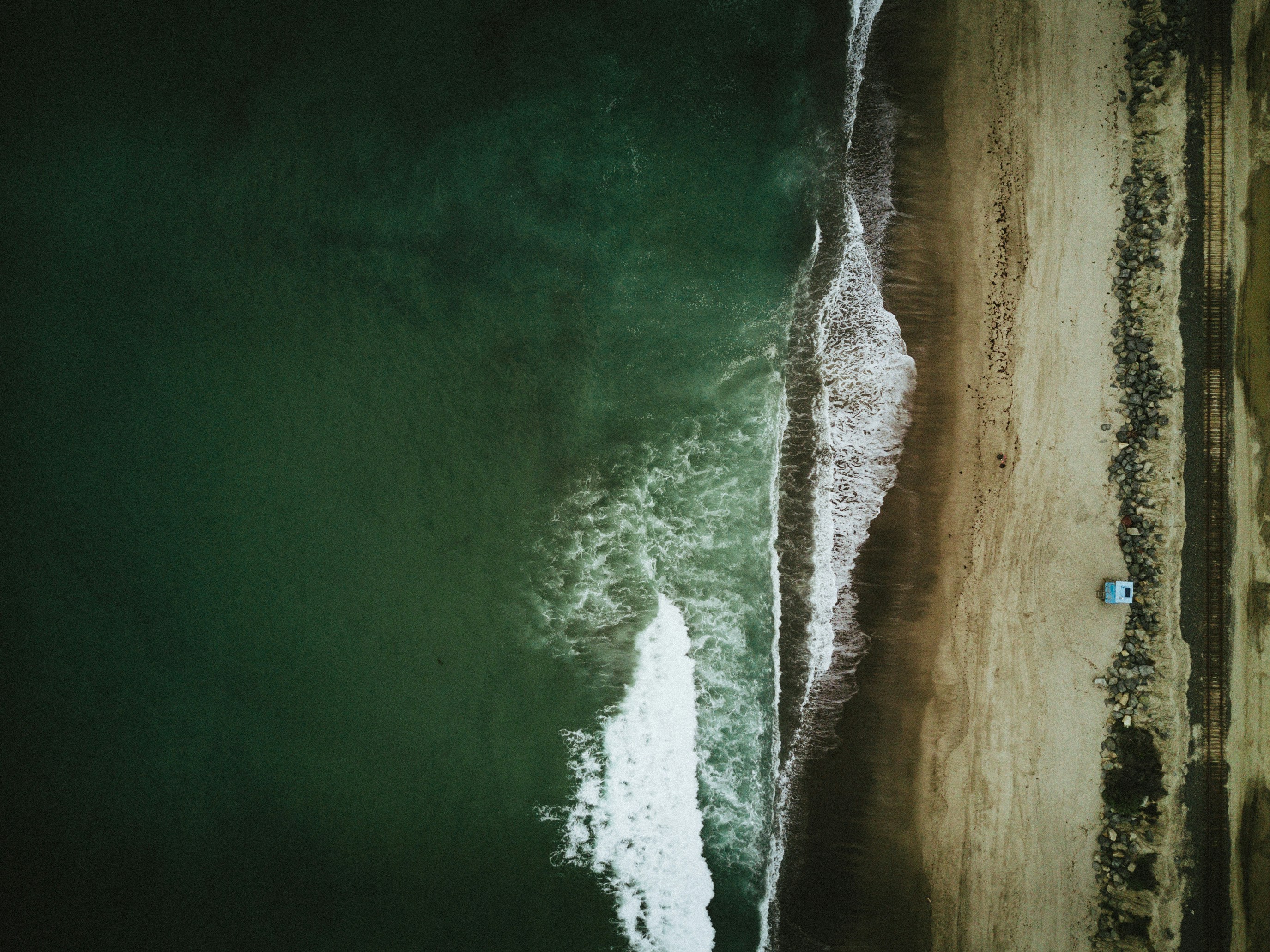 Drone captures waves meeting sandy beach under overcast skies.