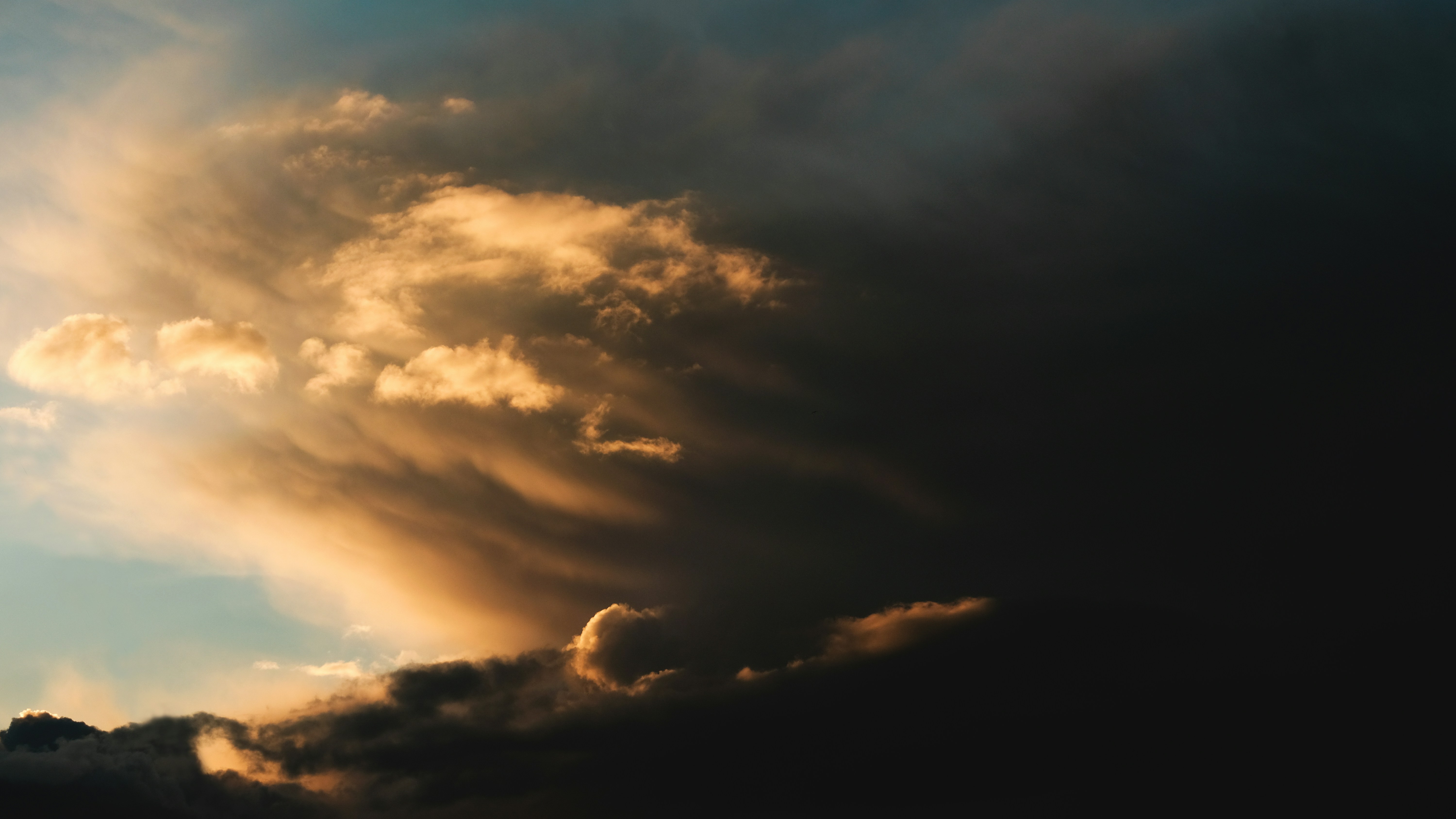Dramatic clouds illuminated by the setting sun, casting a warm glow against the dark sky.