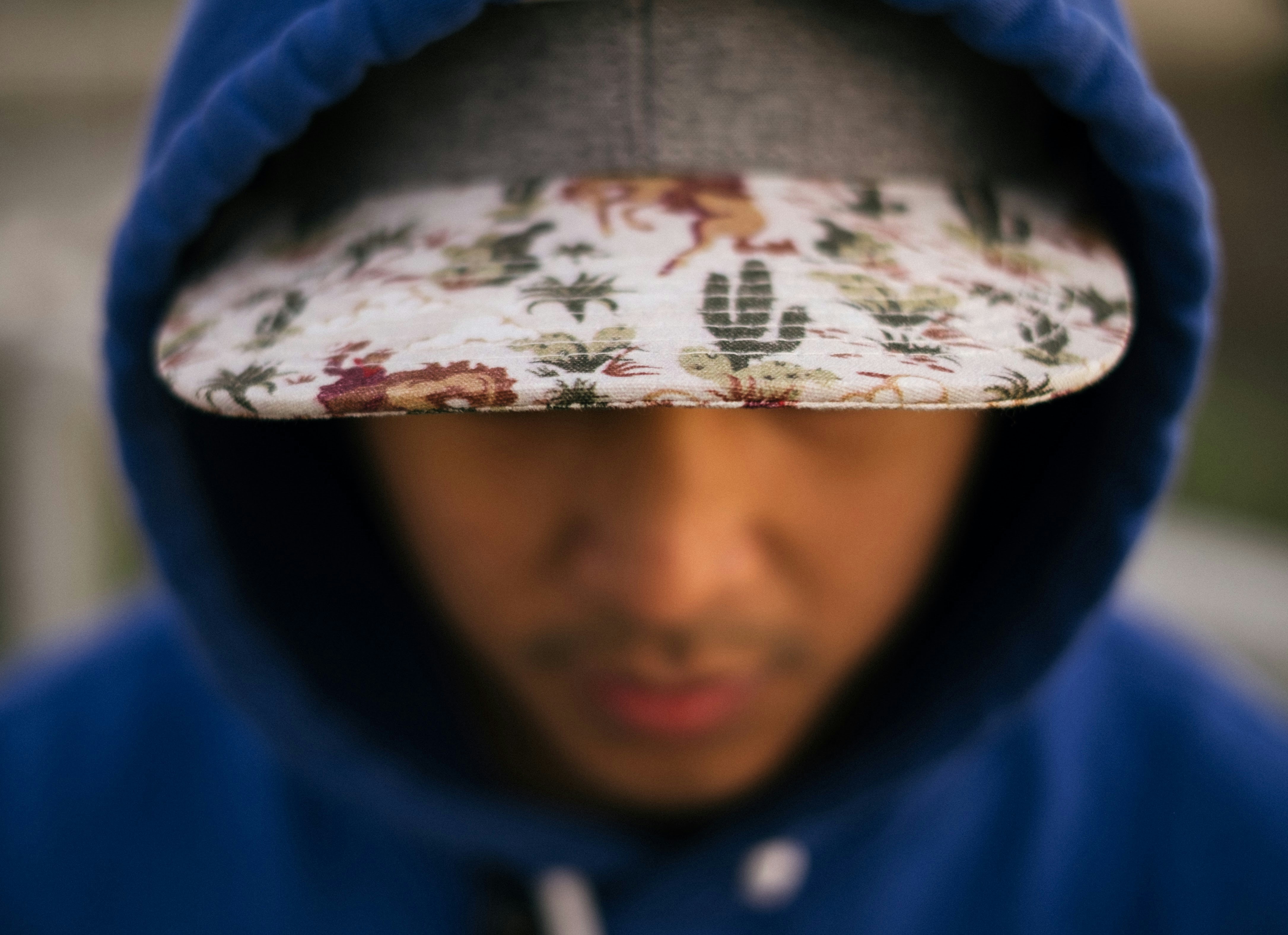 Person wearing a blue hoodie with a floral-patterned baseball cap.