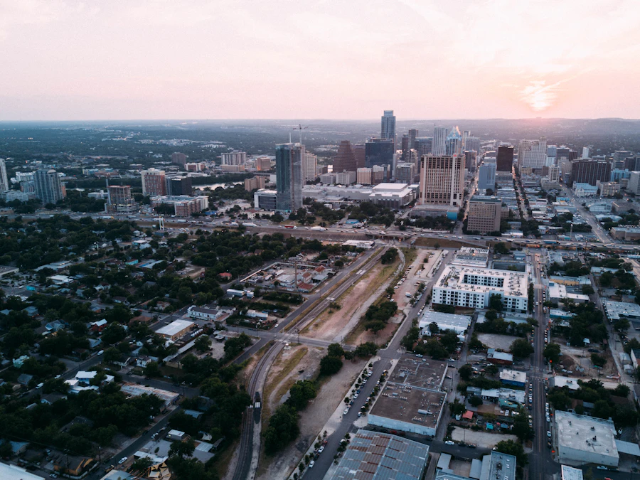 Cityscape at sunset featuring a blend of skyscrapers and residential areas under a soft pink sky.