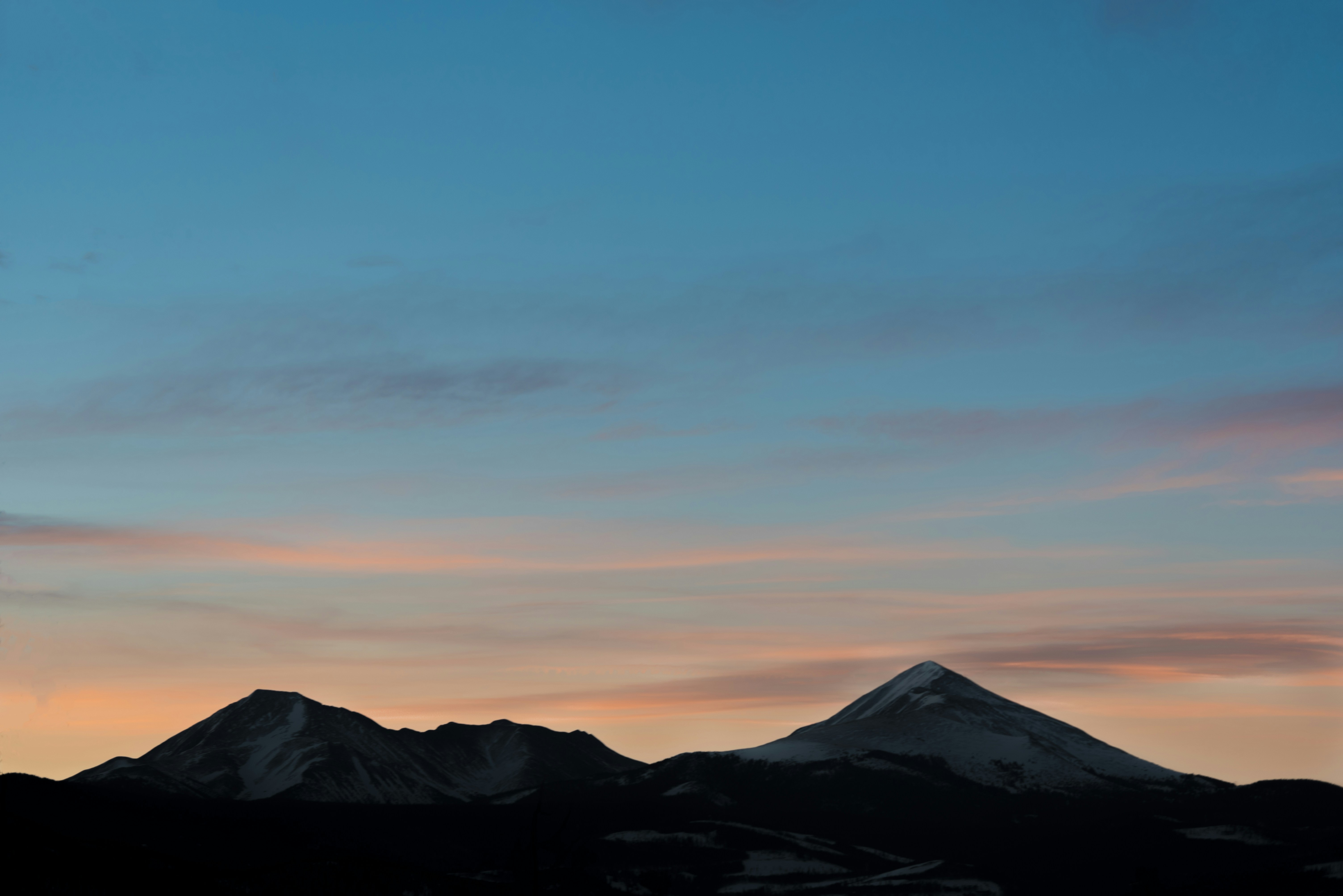 Two majestic mountains silhouetted against a twilight sky, showcasing a gradient of soft colors as day transitions to night.