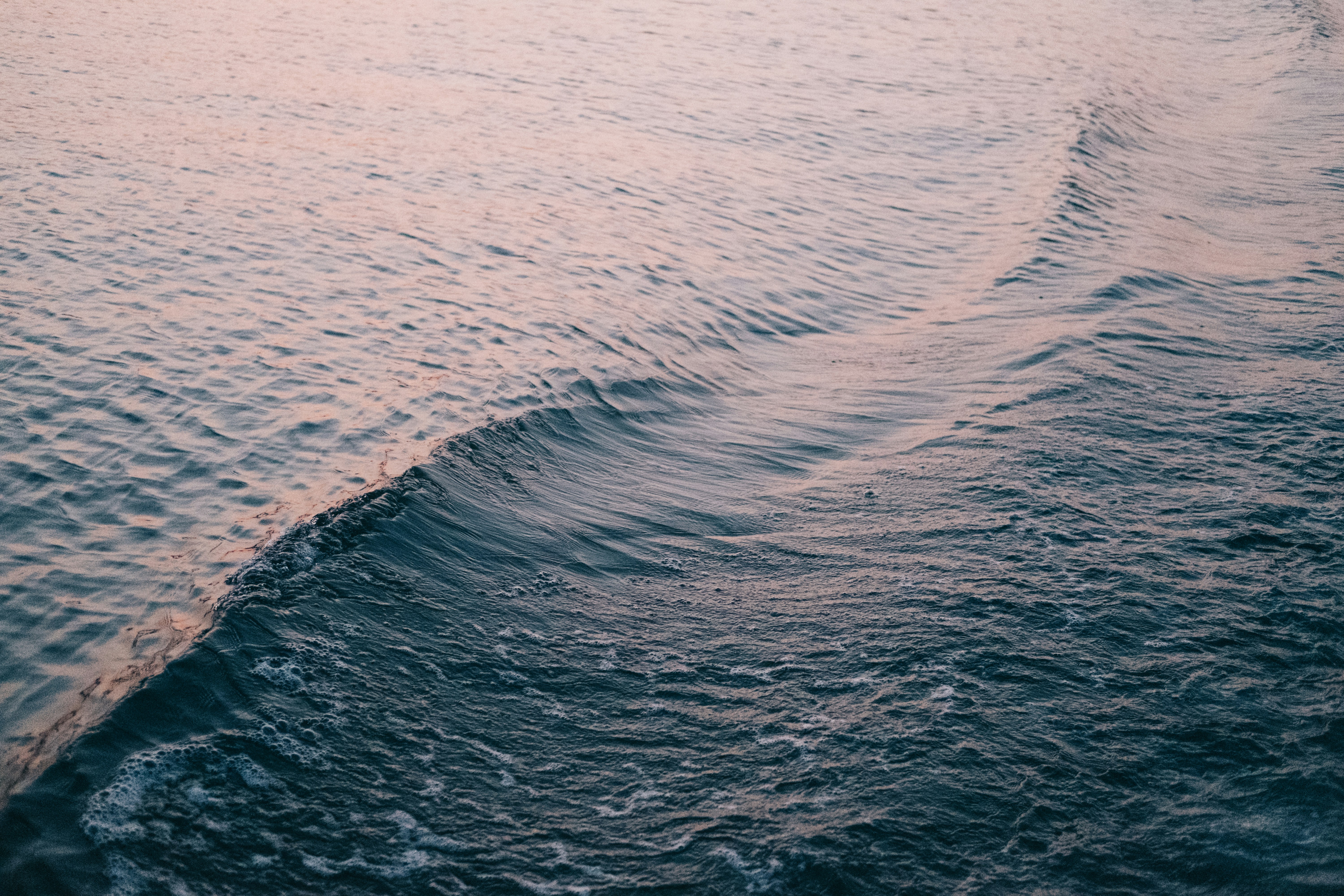 Gentle sea waves ripple under a soft pink sky at sunset.
