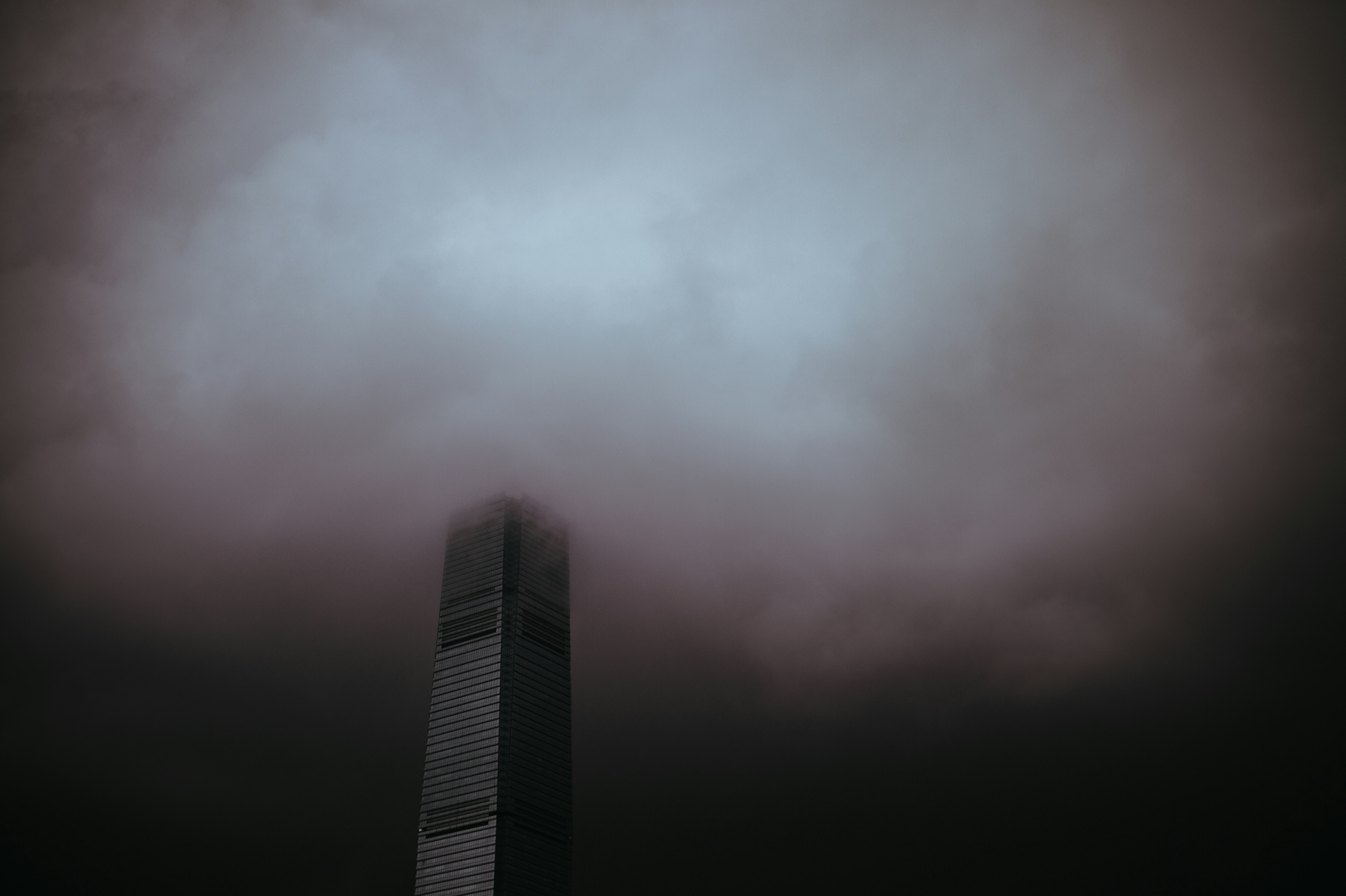 A towering skyscraper emerges from swirling clouds, hinting at the mysteries above. The contrast between the structure and the darkened sky creates a dramatic atmosphere.