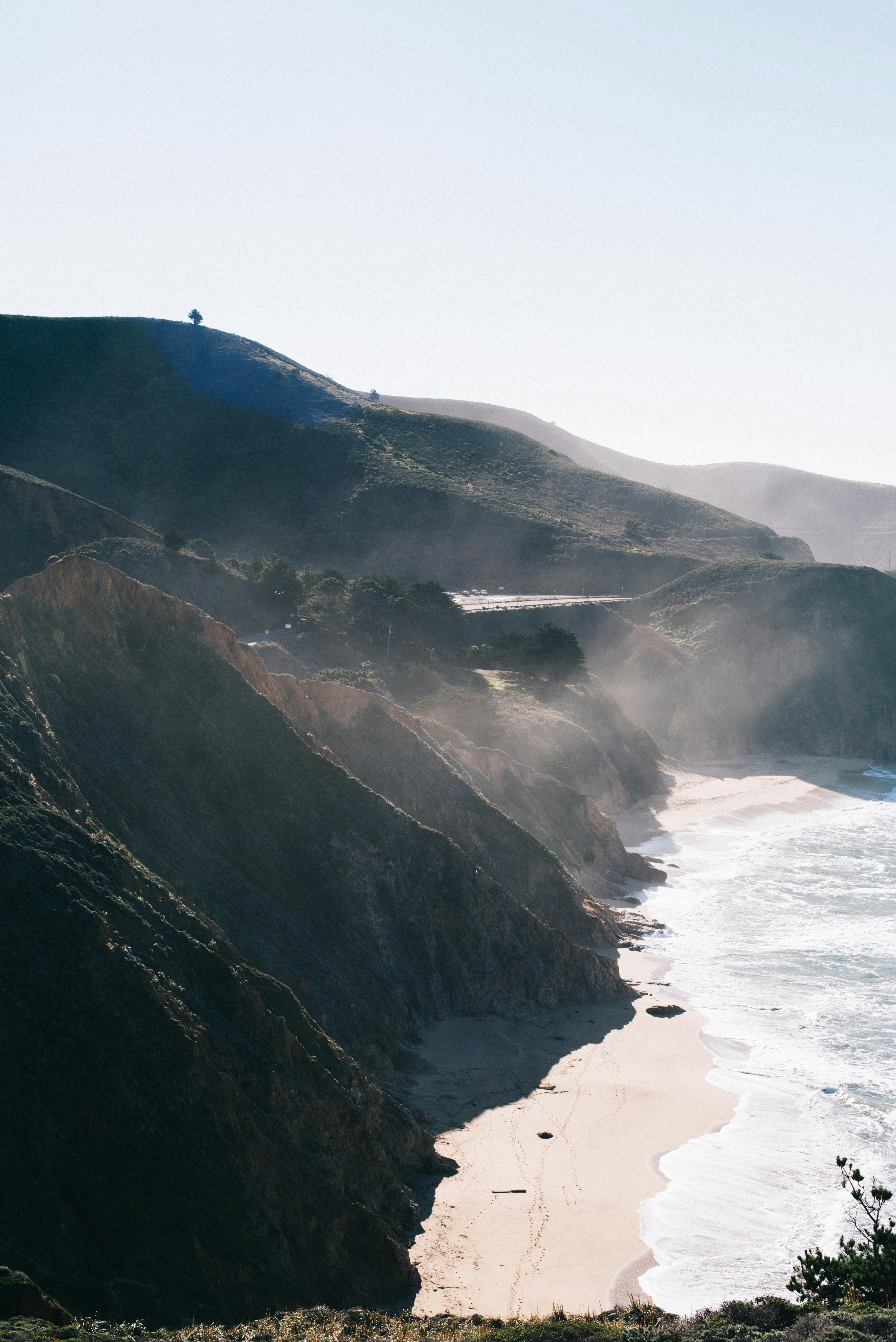 Dramatic coastal cliffs meeting a serene beach under soft sunlight, with mist rising from the shoreline.