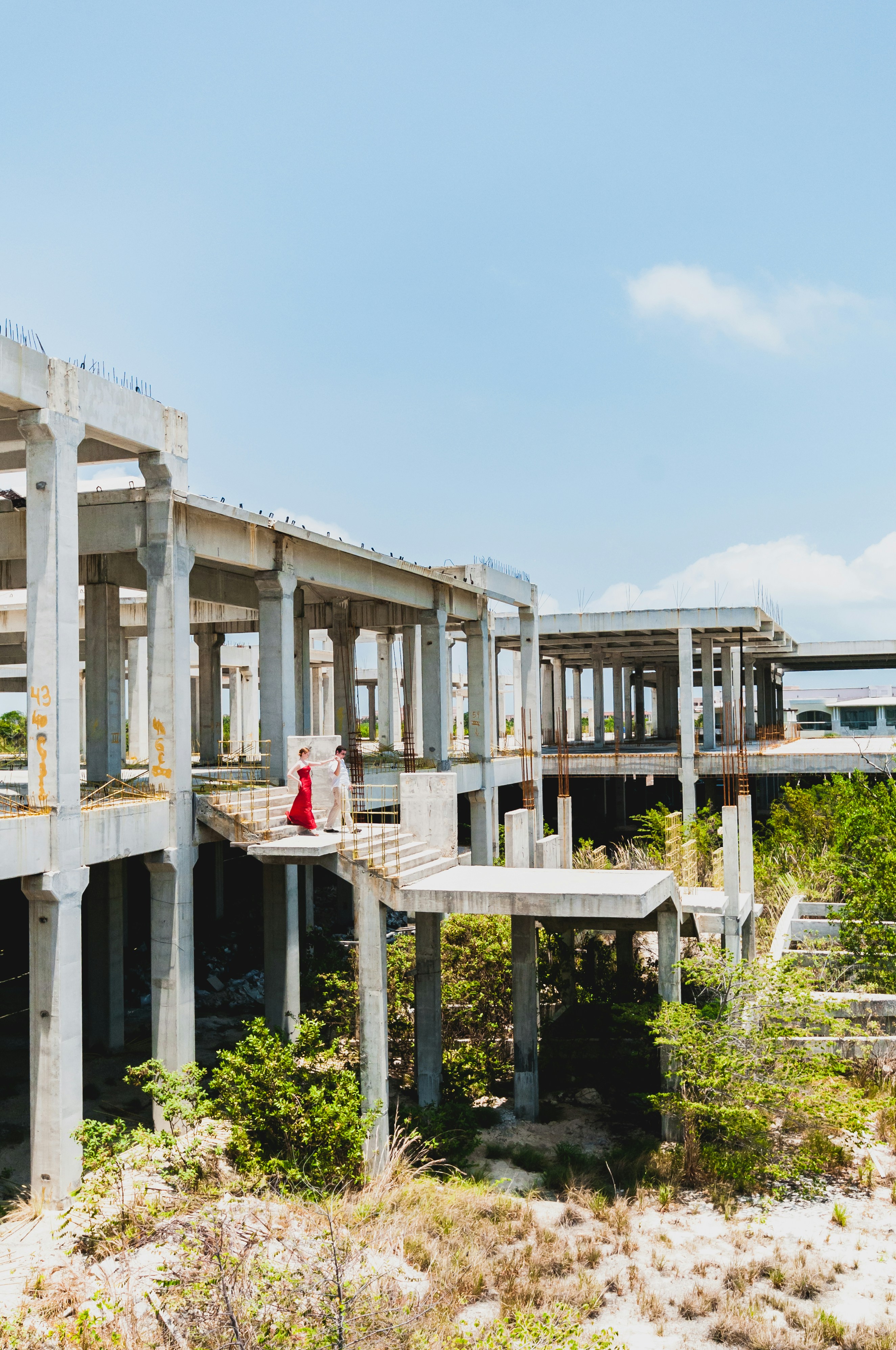 Red Dresses on a Ghostly Staircase Amid Concrete Frames
