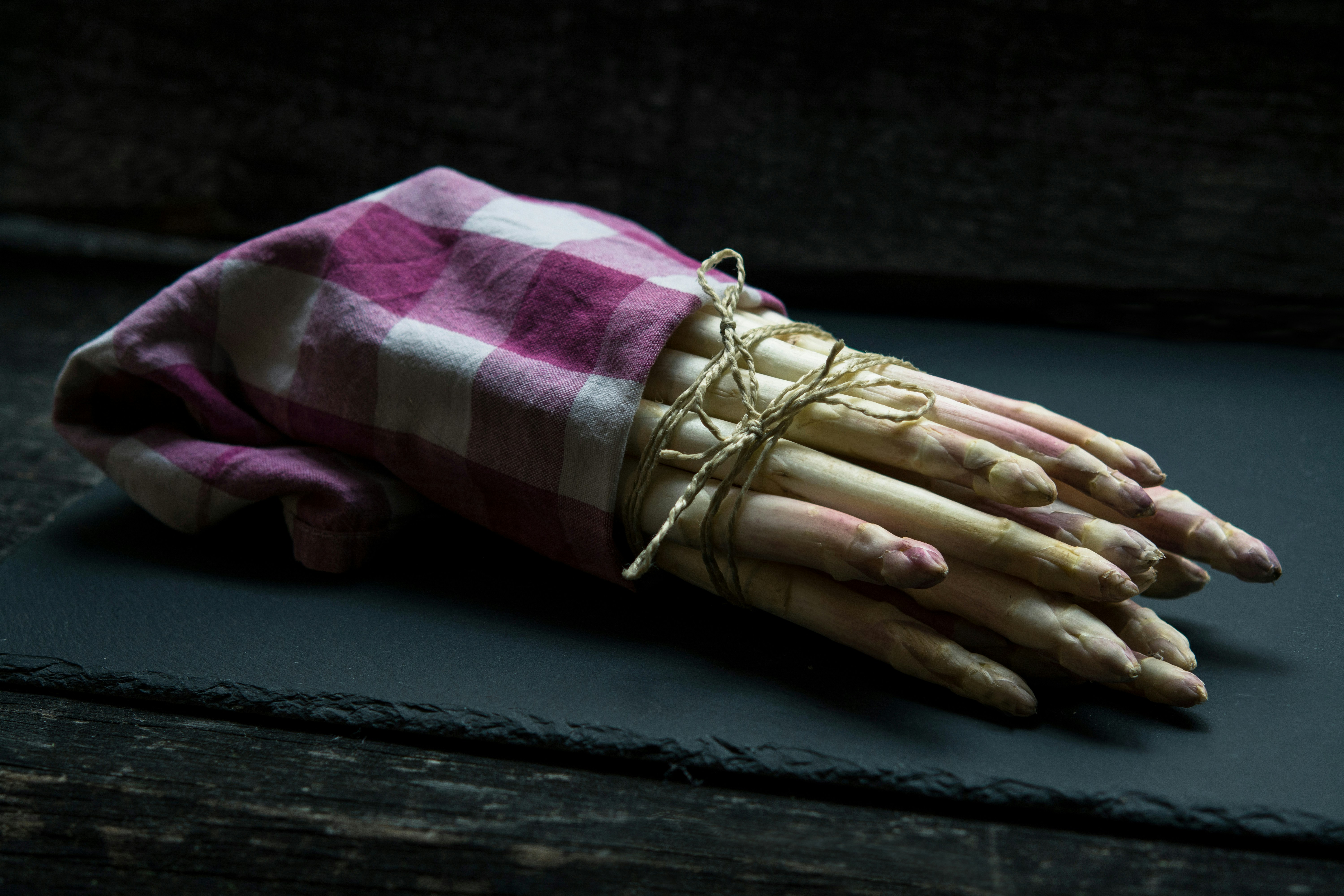 Asparagus bundled in a checkered cloth, resembling a hand, resting on a dark surface.