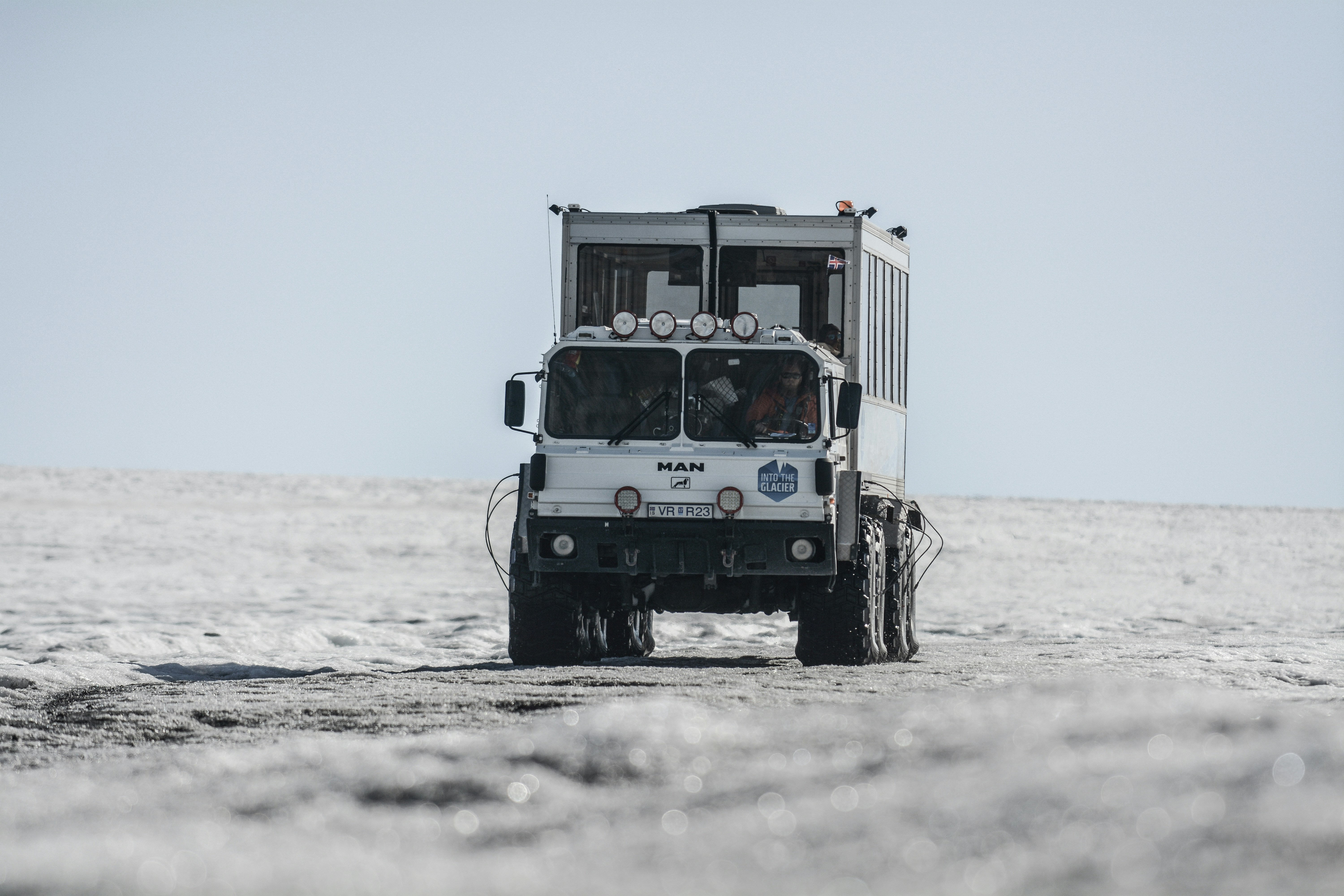 Large expedition vehicle traversing a stark, icy landscape.