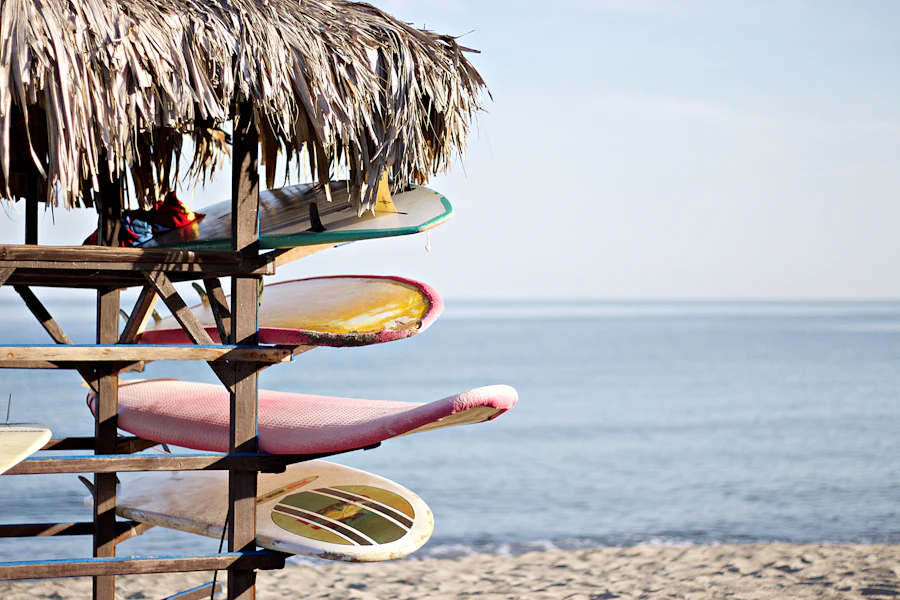 Surfboards stacked under a thatched roof by a calm ocean shore.