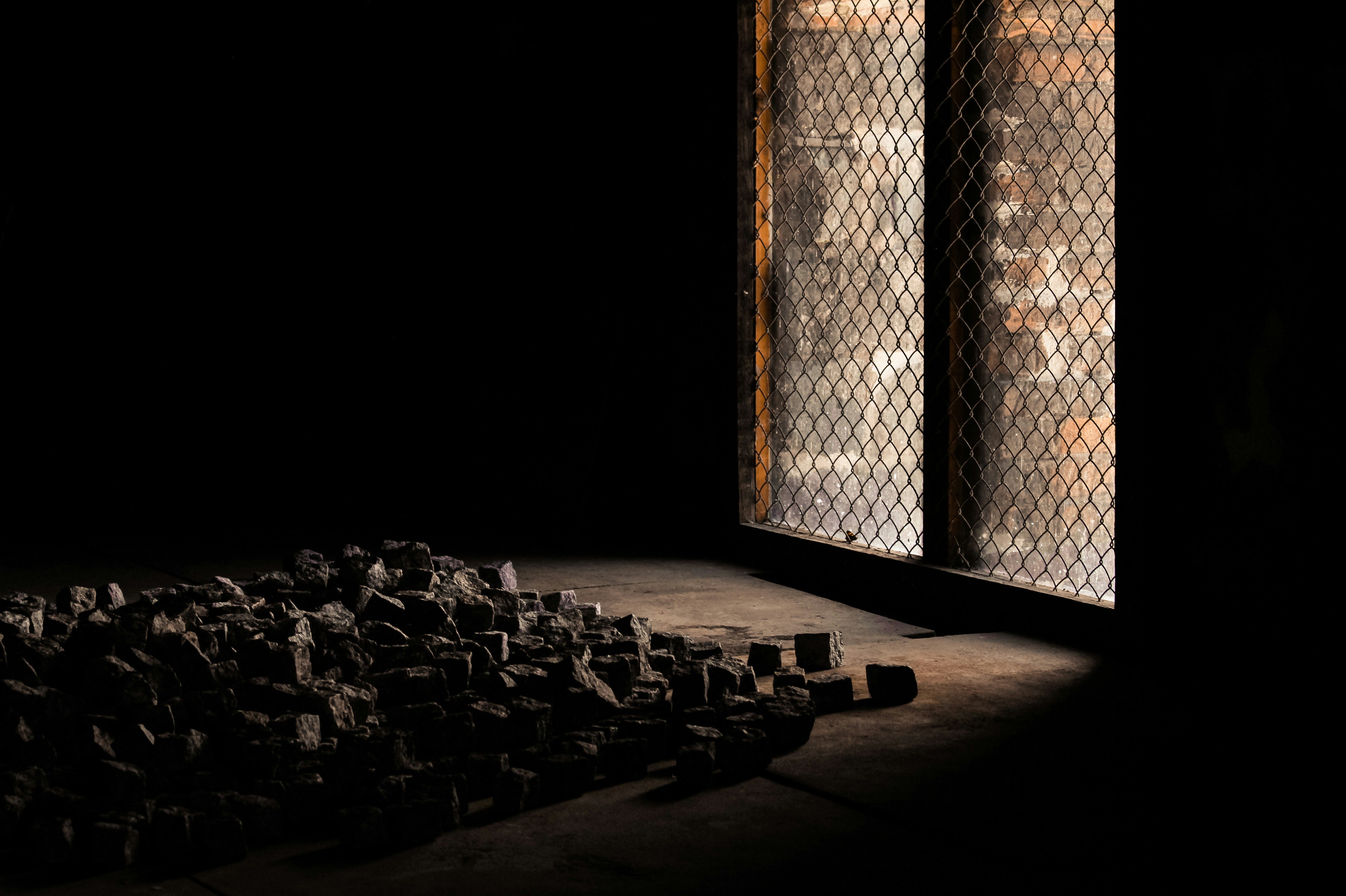 Pile of cobblestones illuminated by soft light through a patterned window in a dim room.