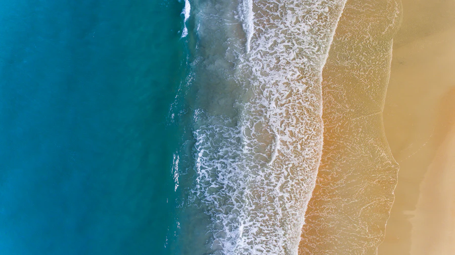 Top-down view of turquoise ocean waves meeting a golden sandy beach, with white foam tracing the shoreline.