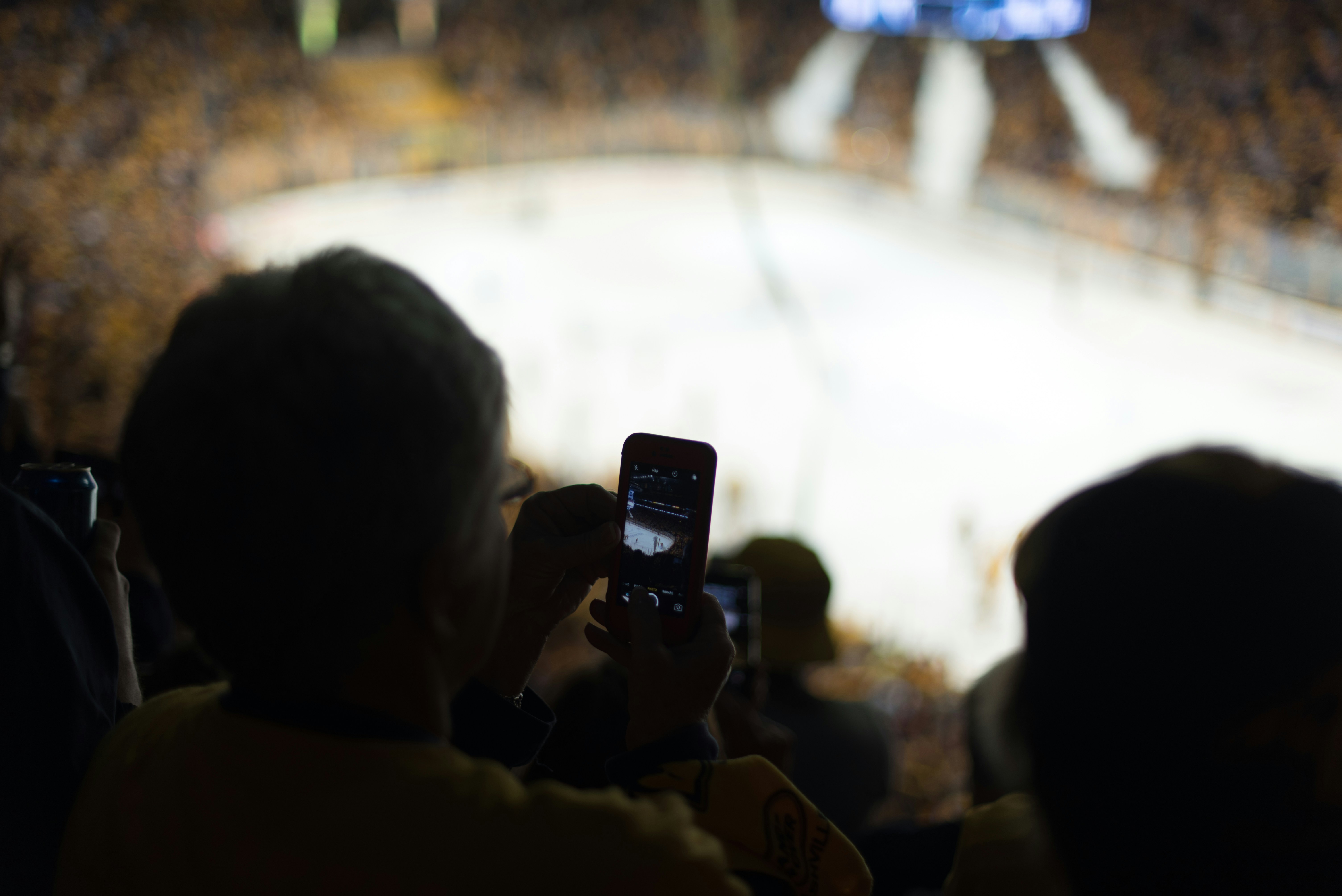 Spectator capturing a live hockey game on a smartphone, surrounded by a sea of enthusiastic fans. 