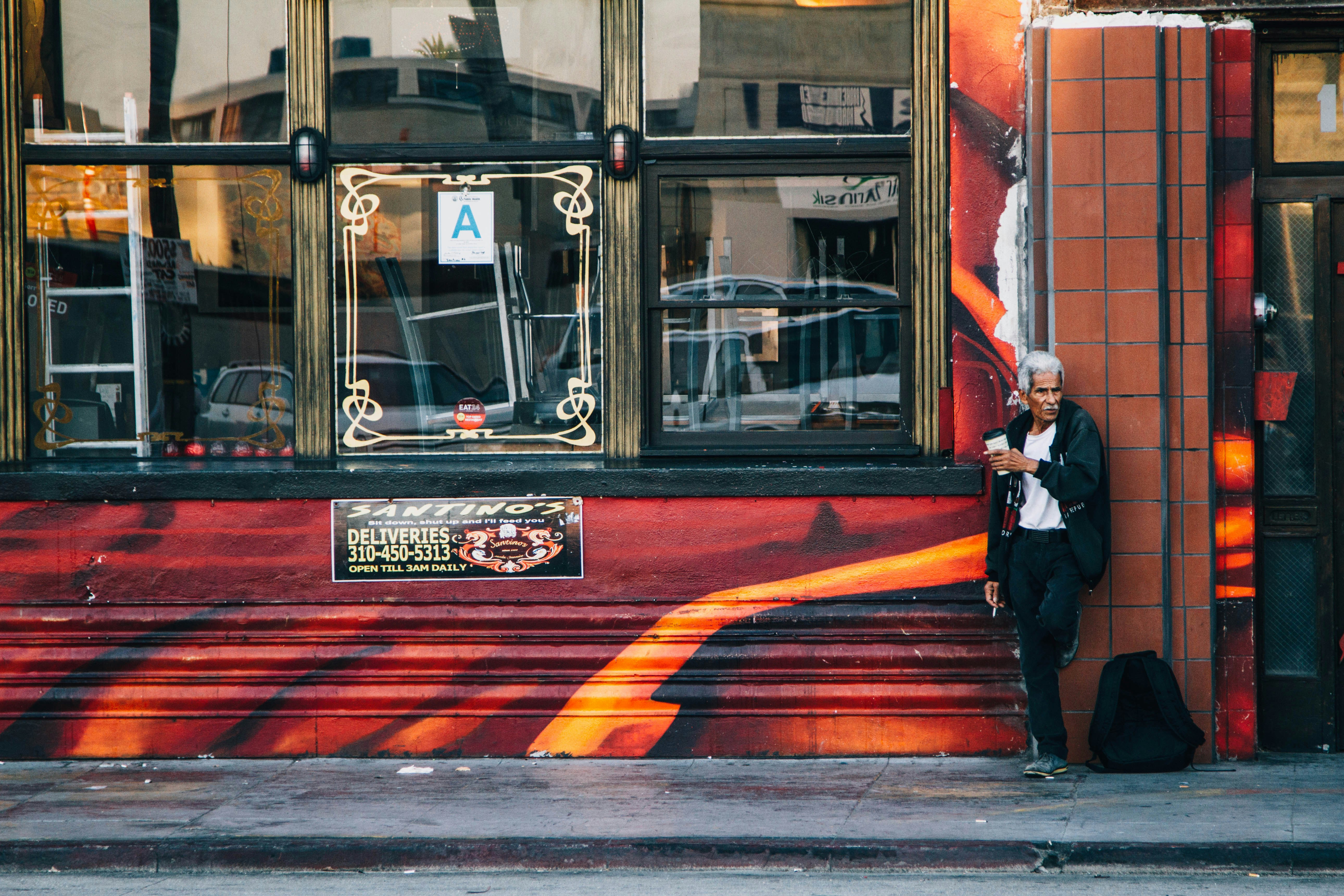 Man leaning against a colorful, graffiti-covered wall holding a cup.