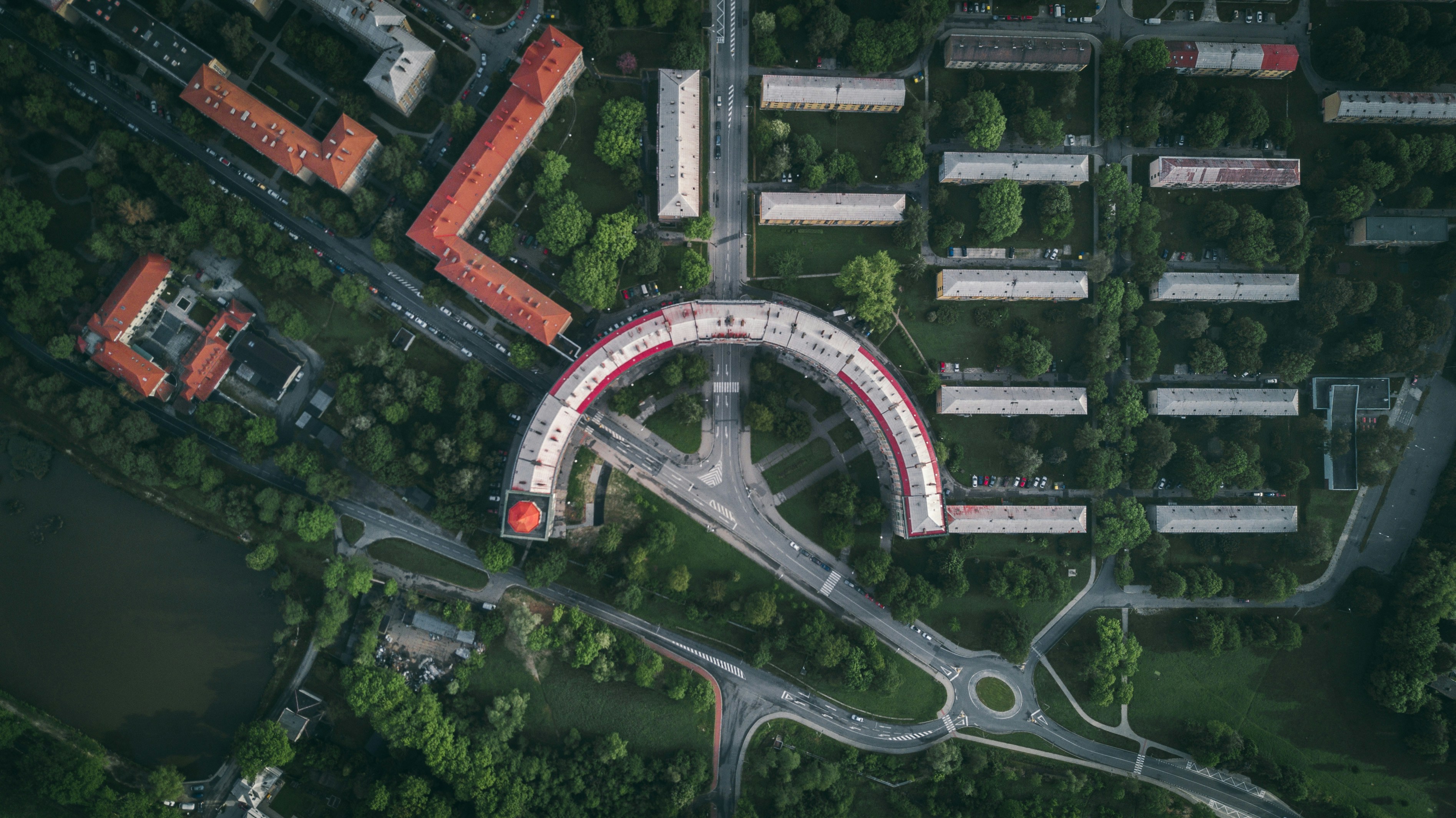 Drone captures unique arc-shaped building surrounded by structured greenery and roads in Ostrava Poruba.