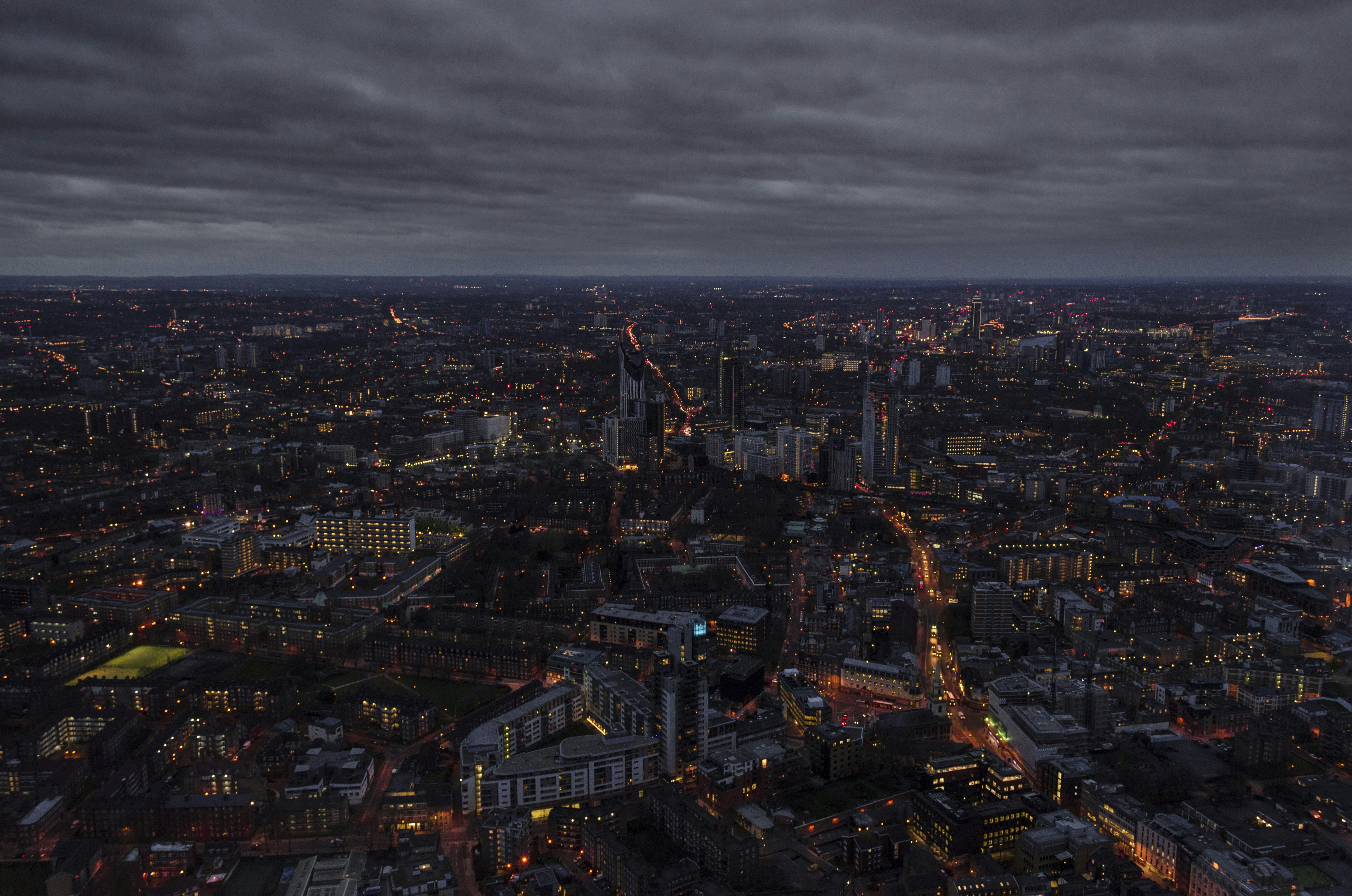 A panoramic view of a bustling city at night, showcasing a network of illuminated streets and towering buildings under a cloudy sky.