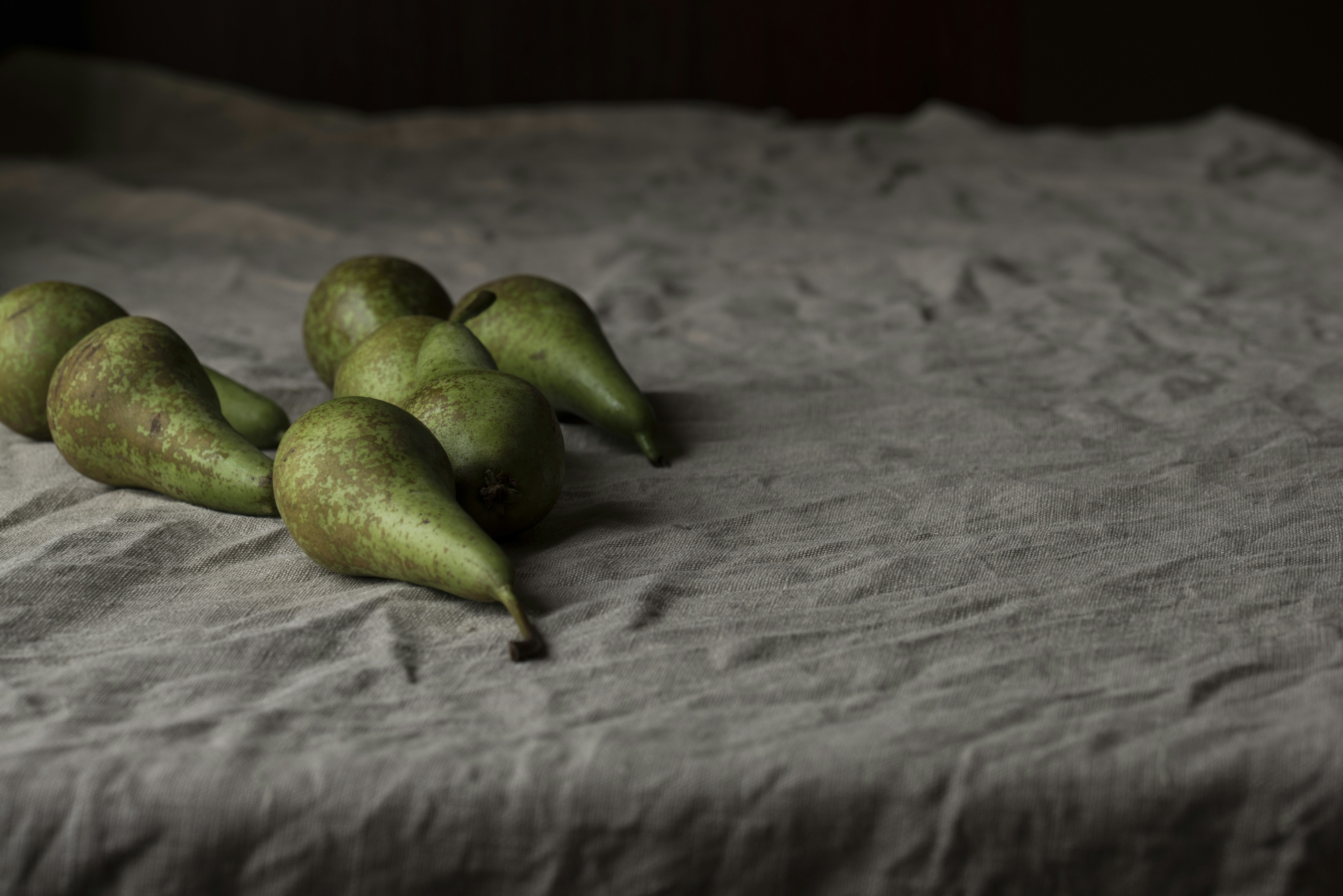 Five green pears arranged on a textured linen cloth, showcasing their natural form and subtle hues.