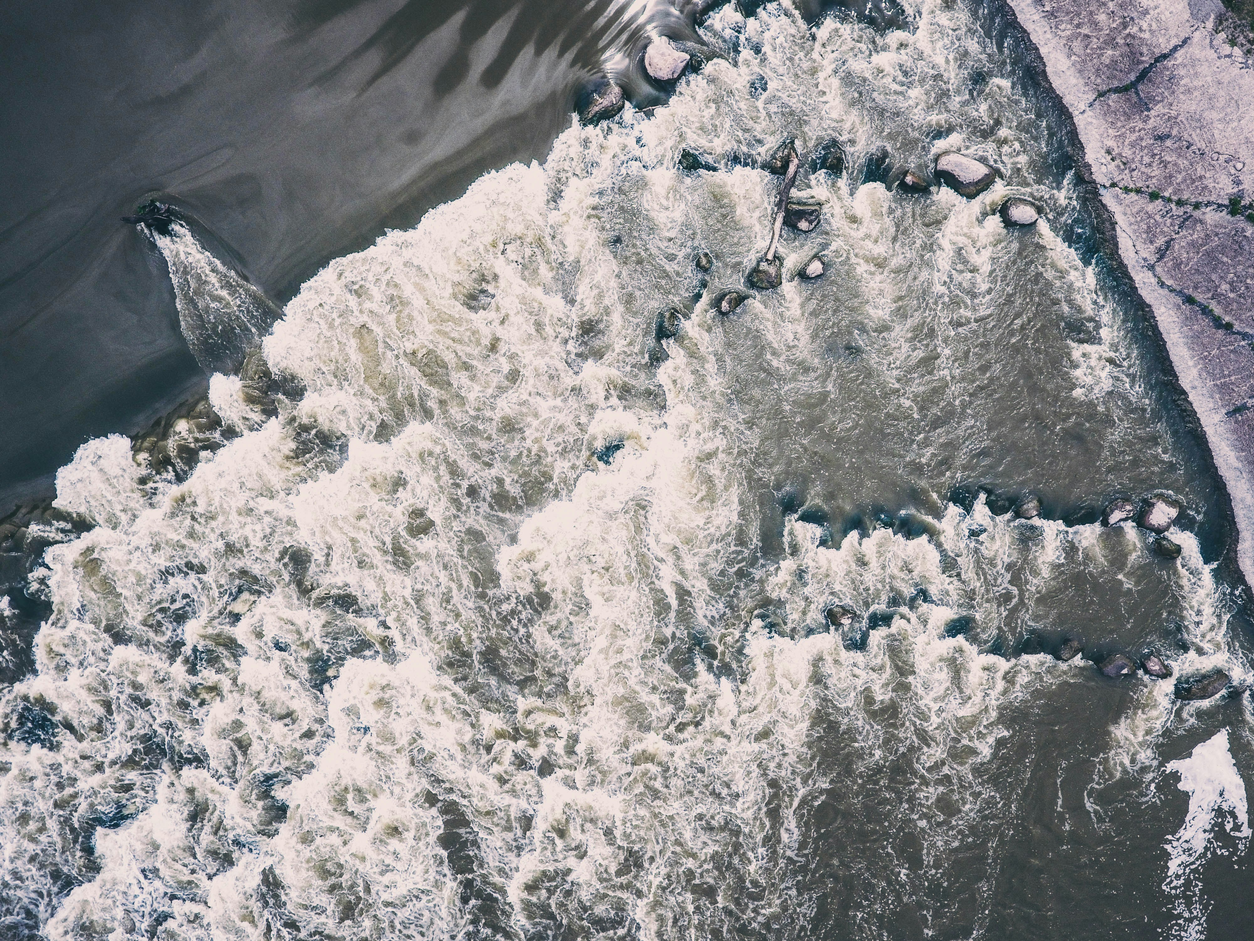 Aerial view of waves crashing over a rocky shoreline, creating intricate patterns of white foam.