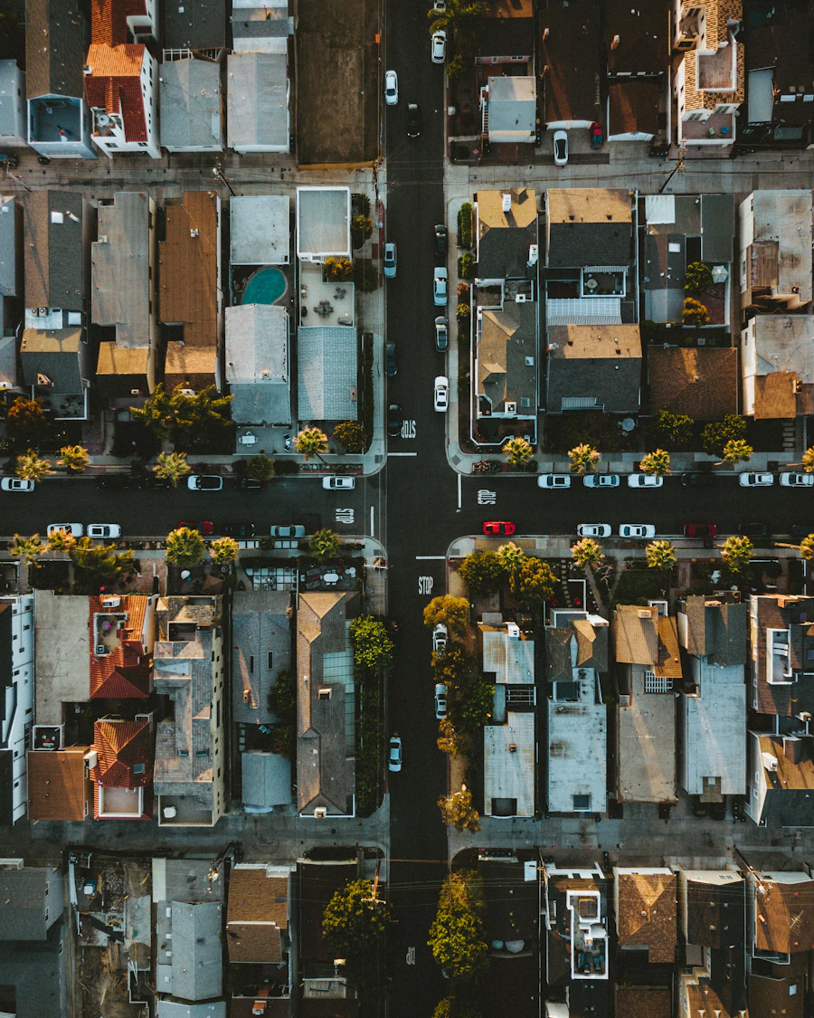 Straight-down aerial view of a residential neighborhood with intersecting streets, parked cars, and tightly packed houses casting warm late-day shadows.