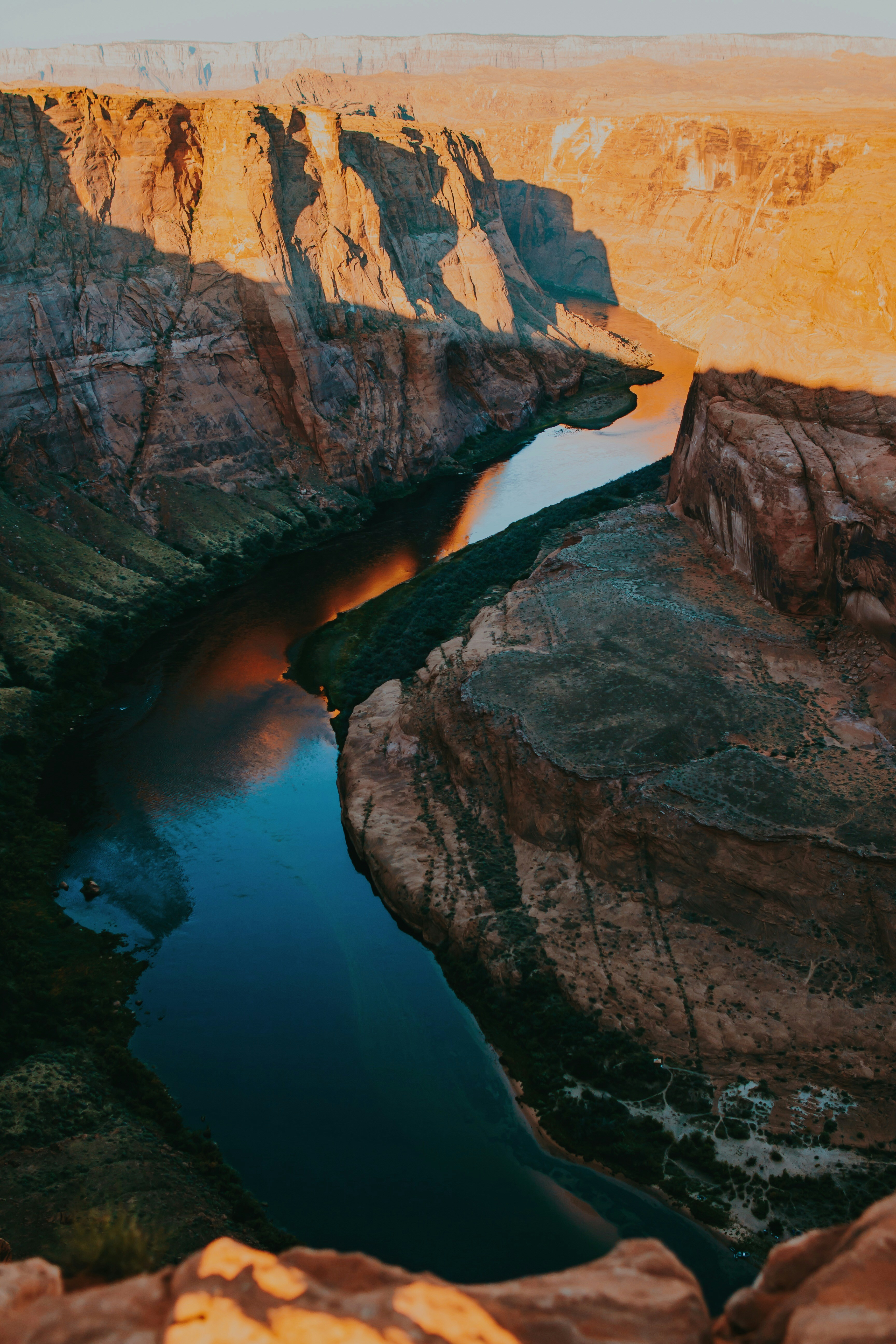 The Colorado River winds through the dramatic canyons, reflecting the warm hues of the setting sun. This landscape captures the raw beauty of nature's sculpting forces.