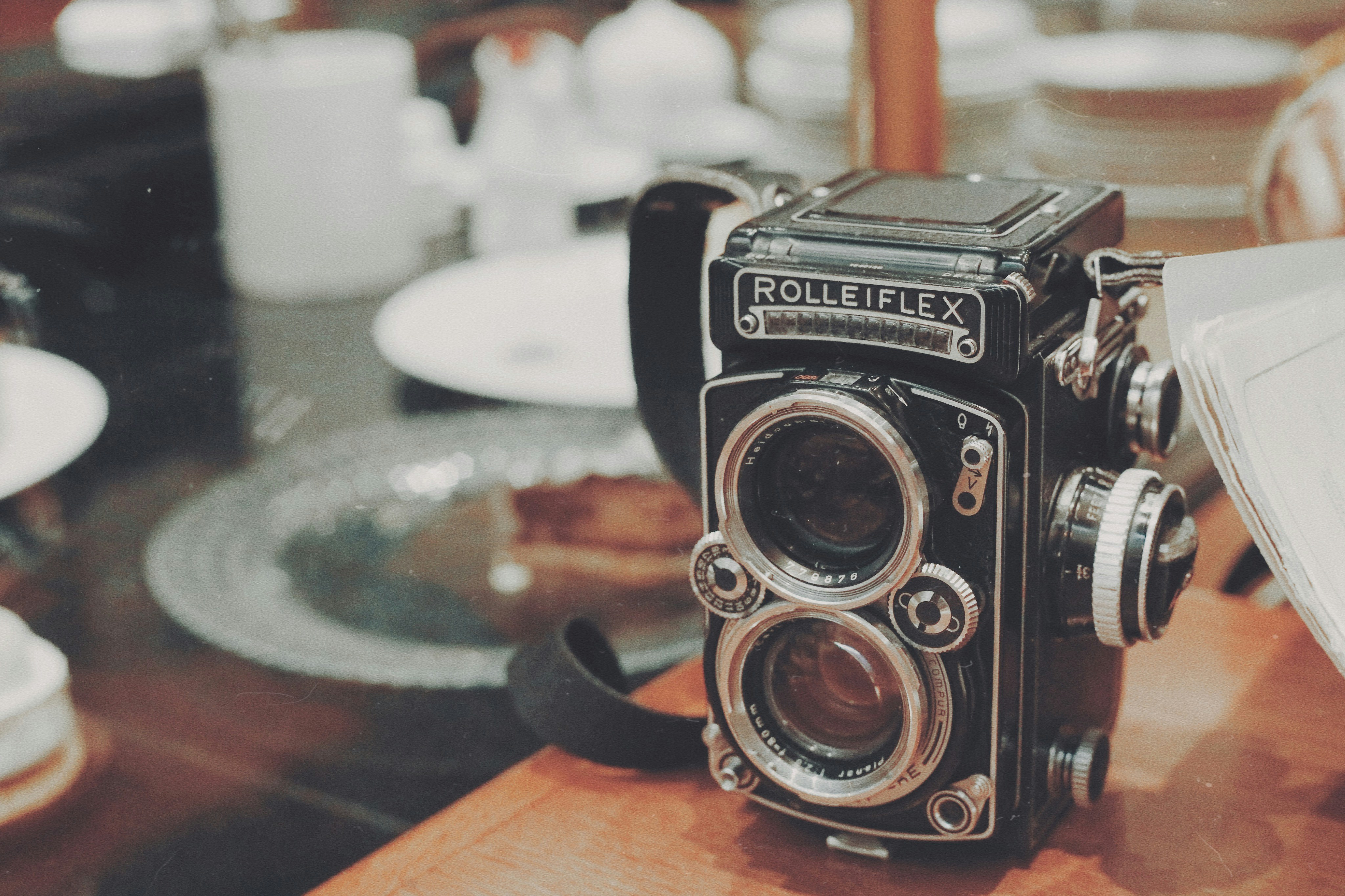 Vintage Rolleiflex camera resting on a reflective glass surface with blurred tableware in the background.