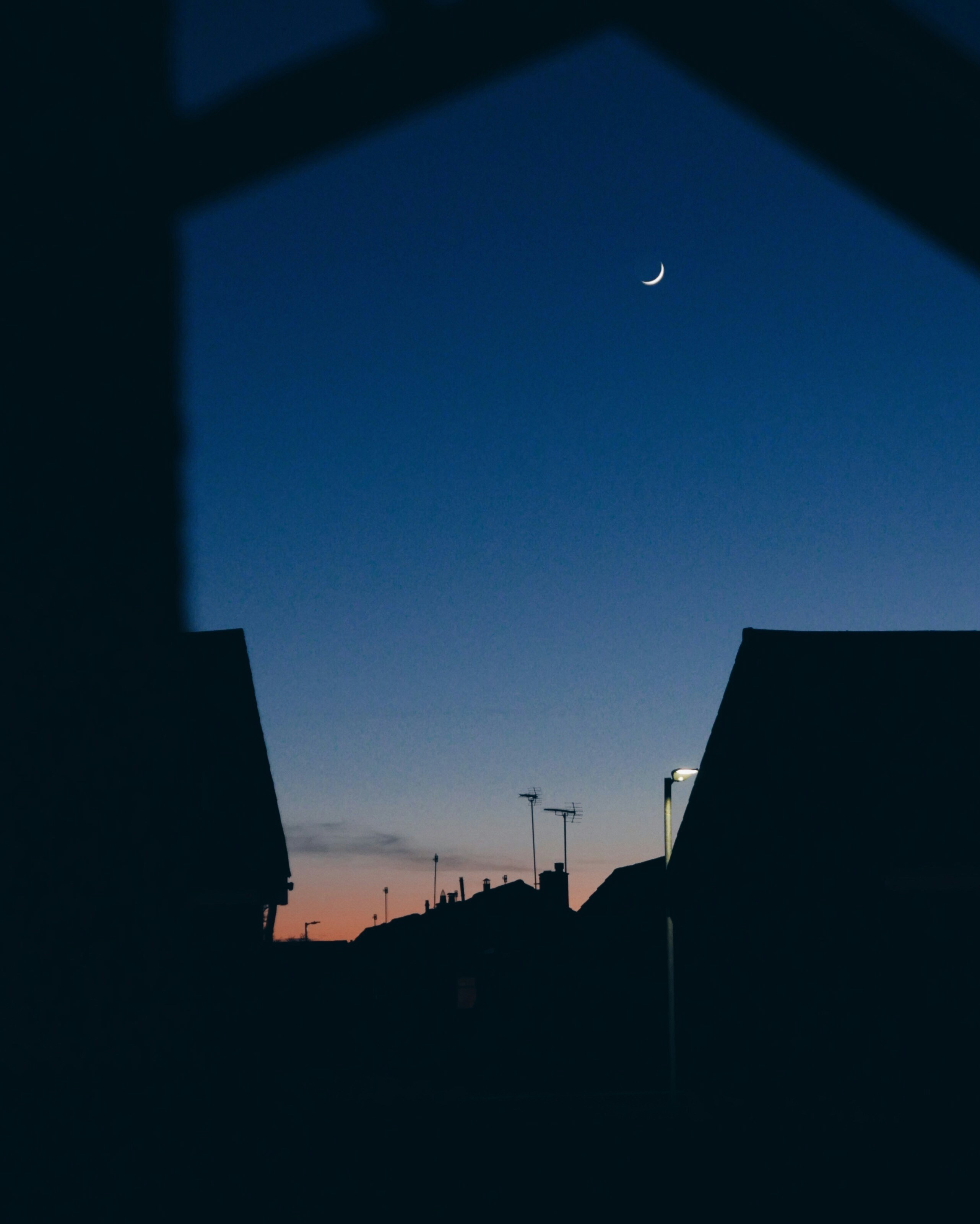 Crescent moon in a twilight sky above silhouetted rooftops and antennas.