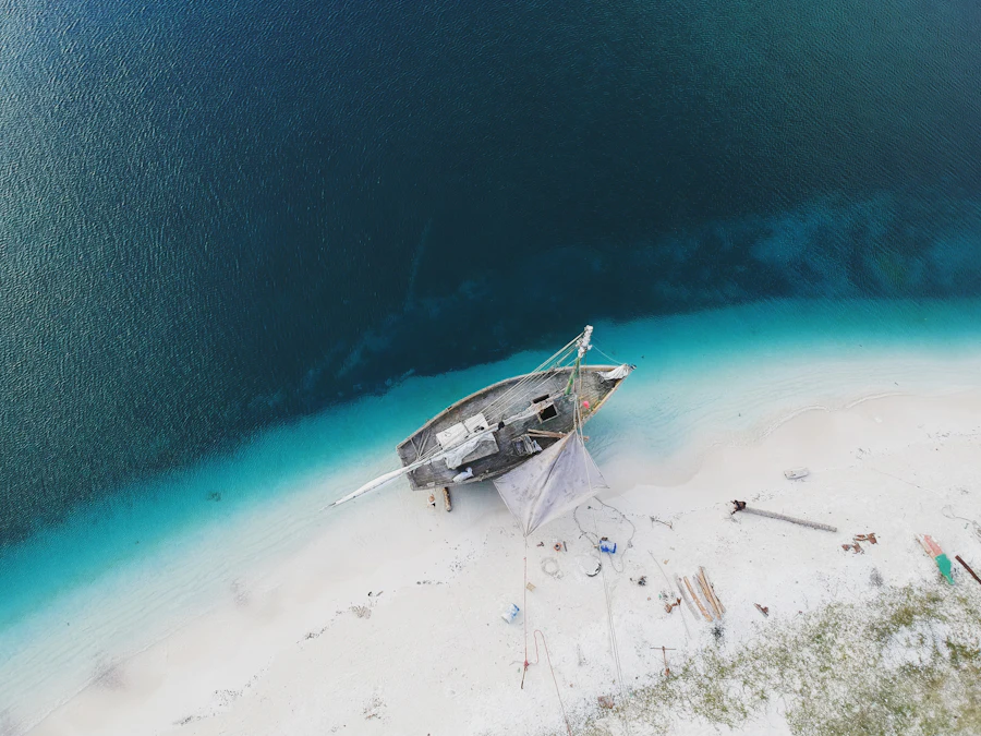 Small wooden boat rests on a bright white sand beach beside a vivid turquoise shallows that fades into deep blue water. Sparse gear and tracks dot the shoreline around it.
