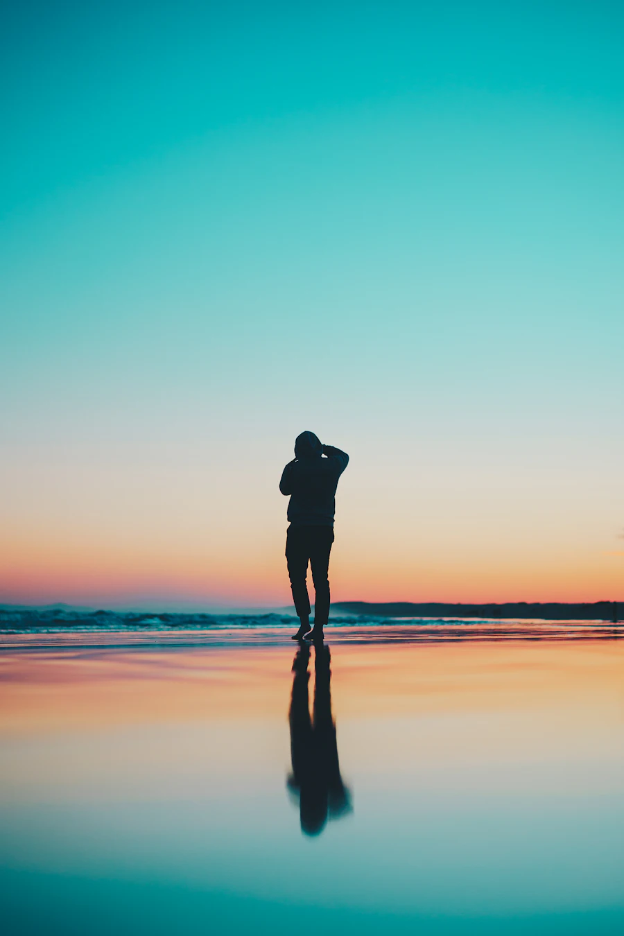 Silhouette of a person standing on a beach, capturing the serene sunset reflected on the water's surface.