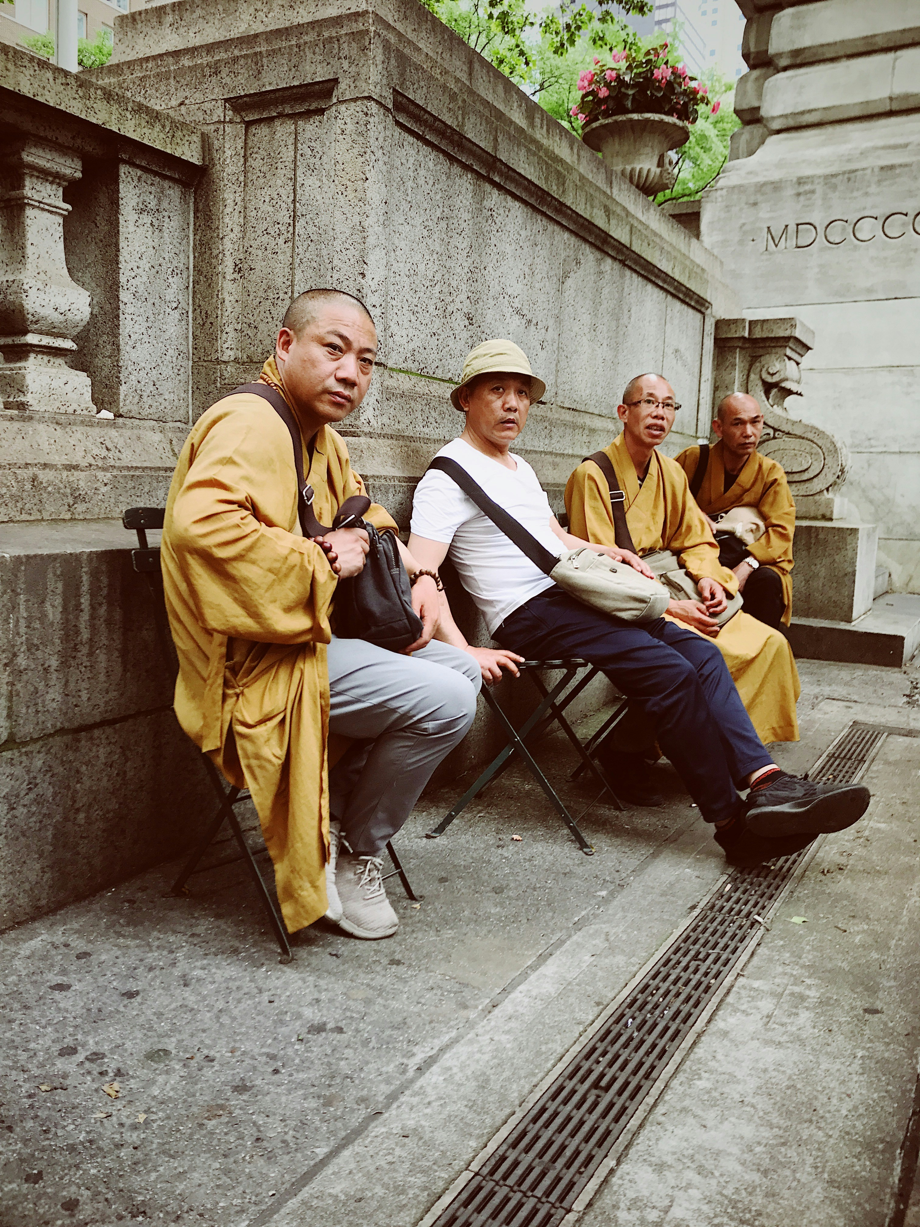 Four individuals in traditional attire seated against a textured stone backdrop, embodying a moment of tranquility amidst city life.