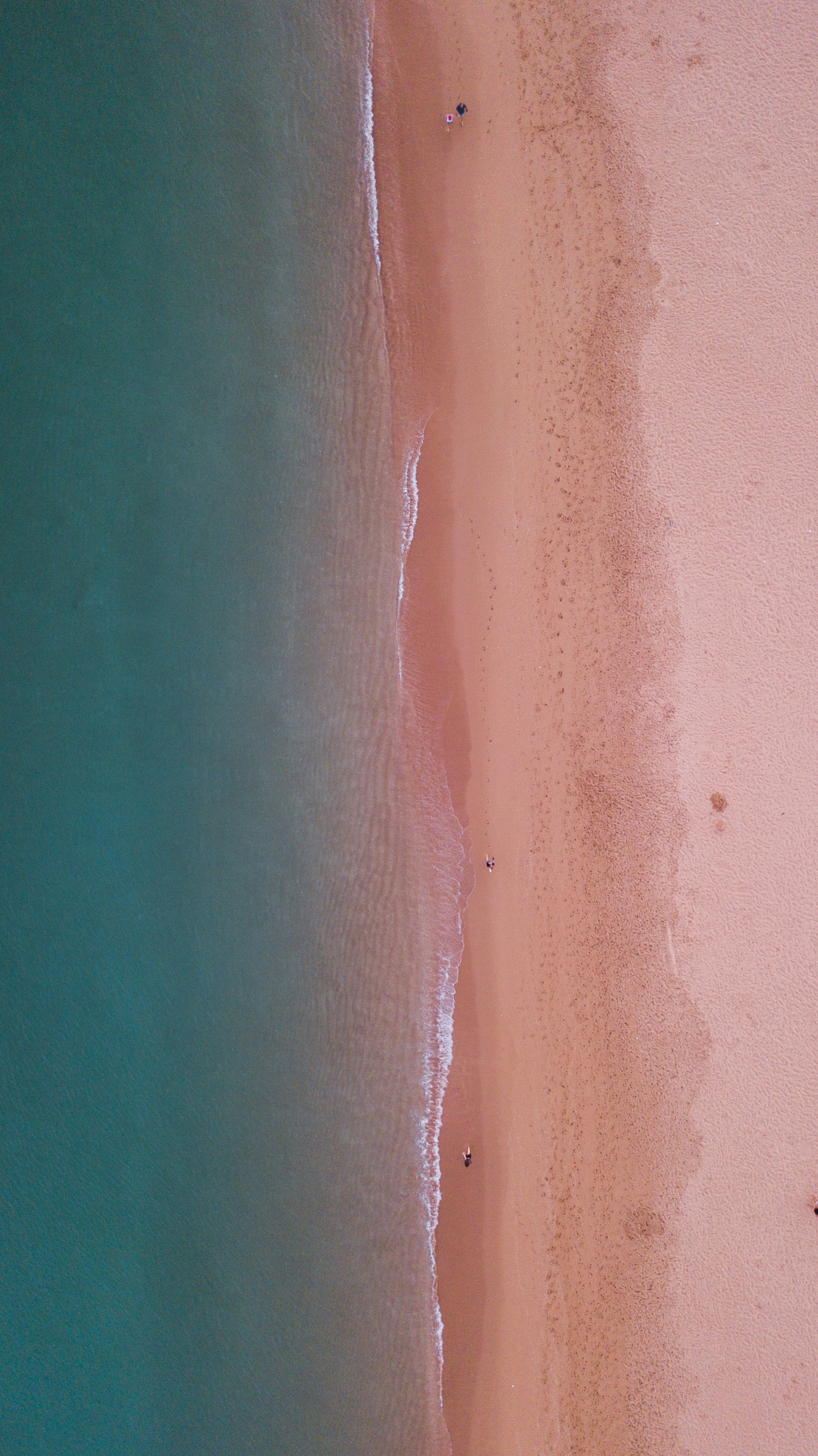 Aerial view of a tranquil beach where soft waves meet golden sands, with a few figures enjoying the serene landscape.