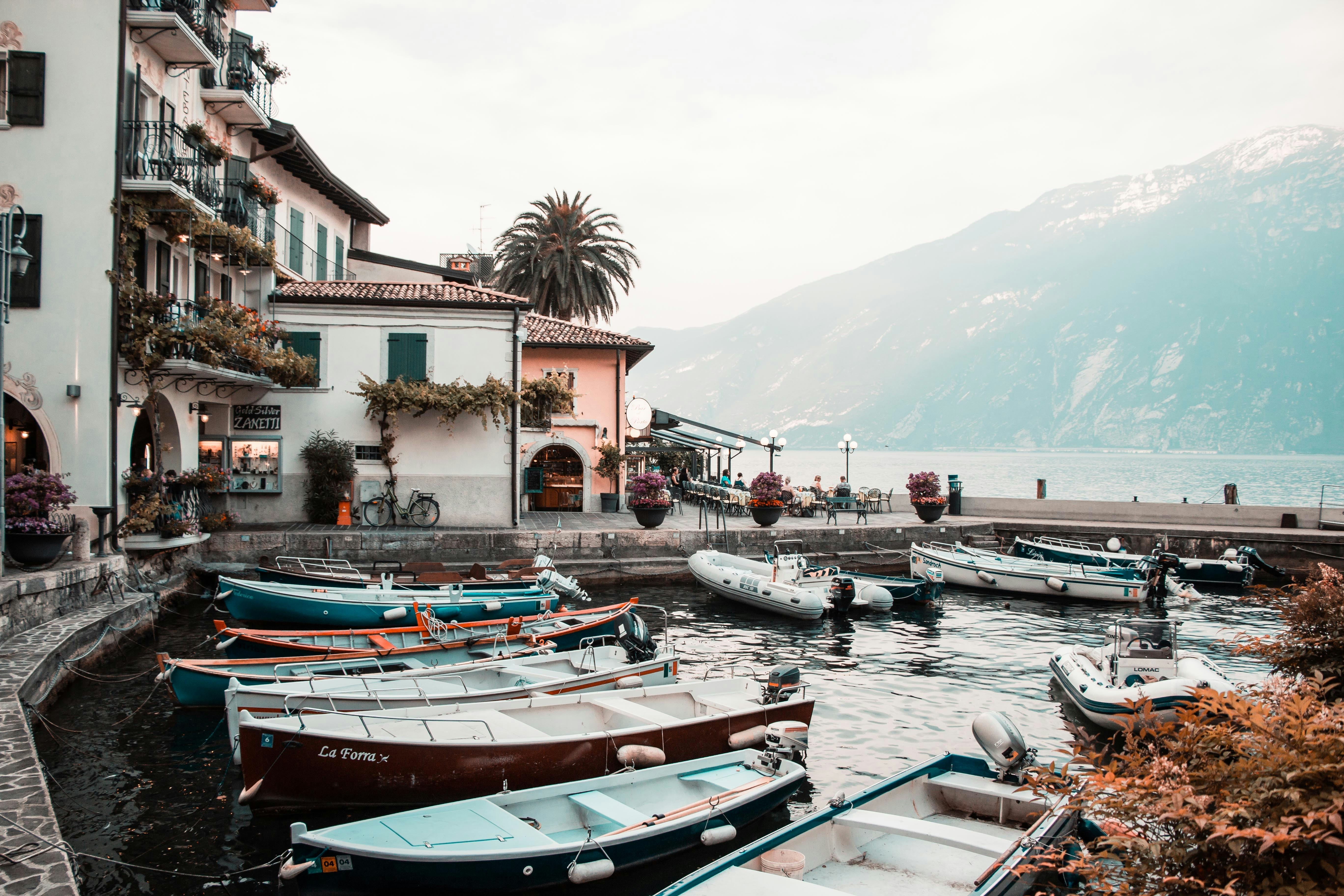 Colorful boats anchored in a tranquil harbor, framed by charming buildings and a picturesque mountain backdrop.