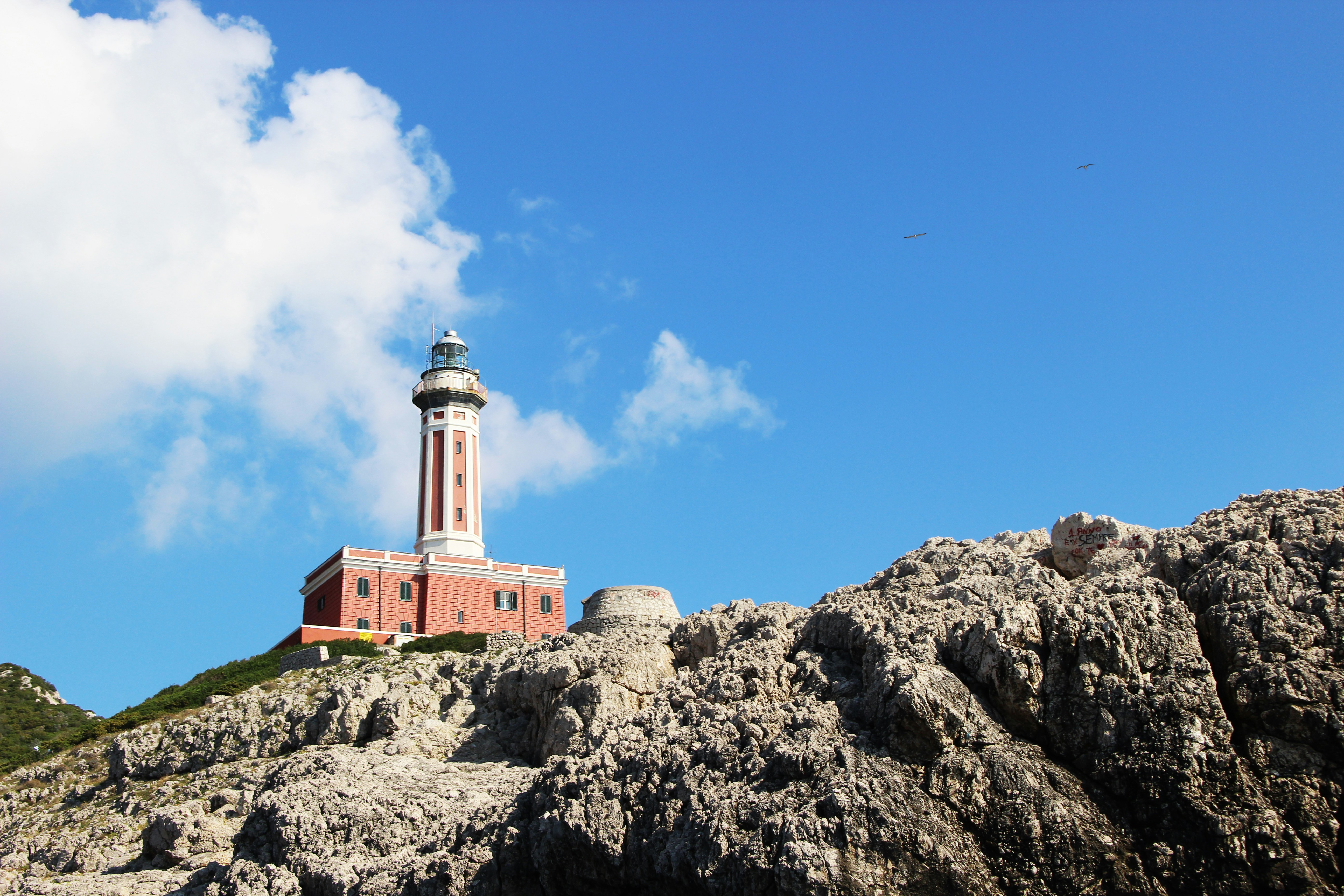 Historic lighthouse perched on rugged cliffs under a bright blue sky, surrounded by rocky terrain. A testament to maritime navigation.