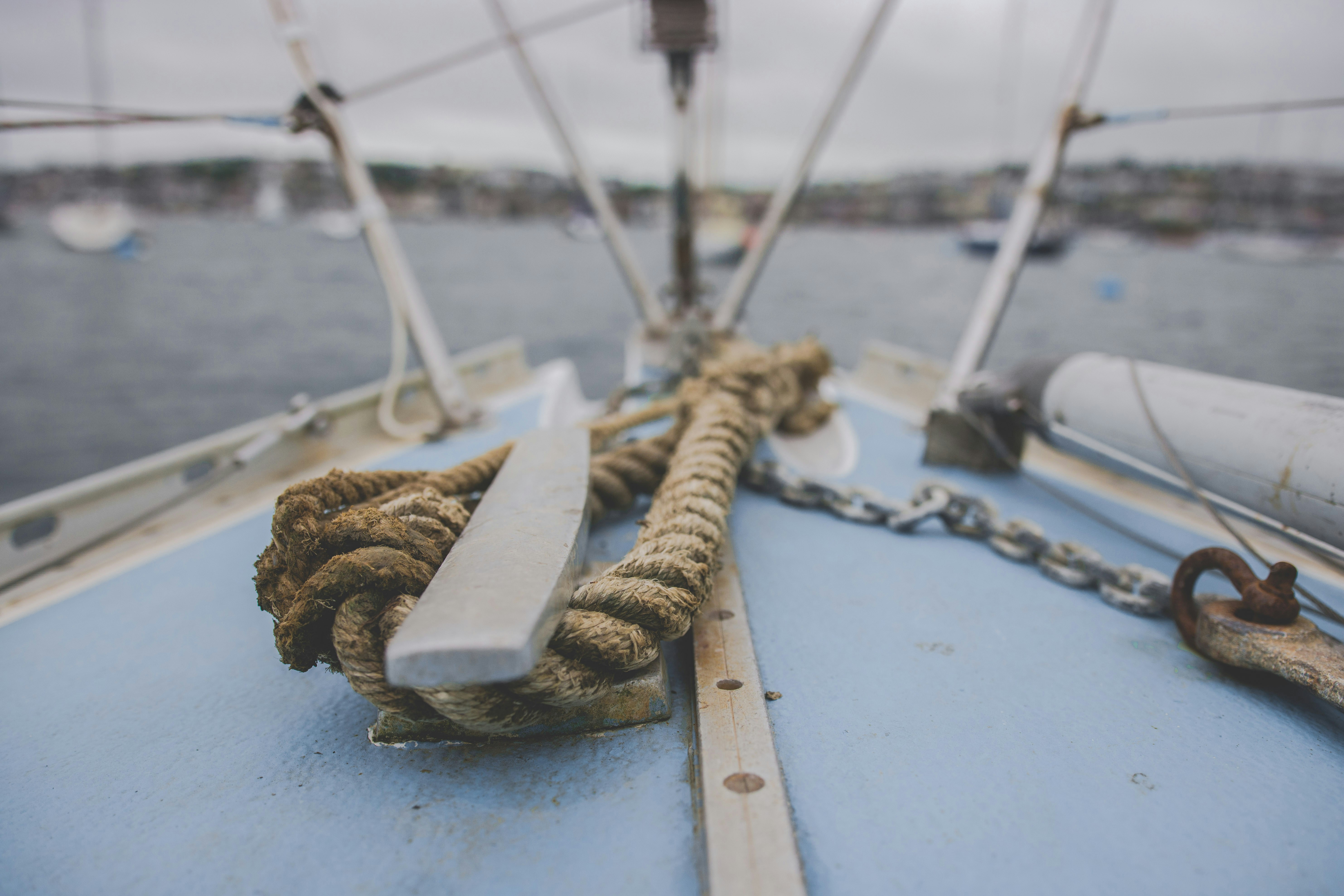 Close-up of a coiled rope on a sailboat deck, with a blurred background of water and distant boats. 