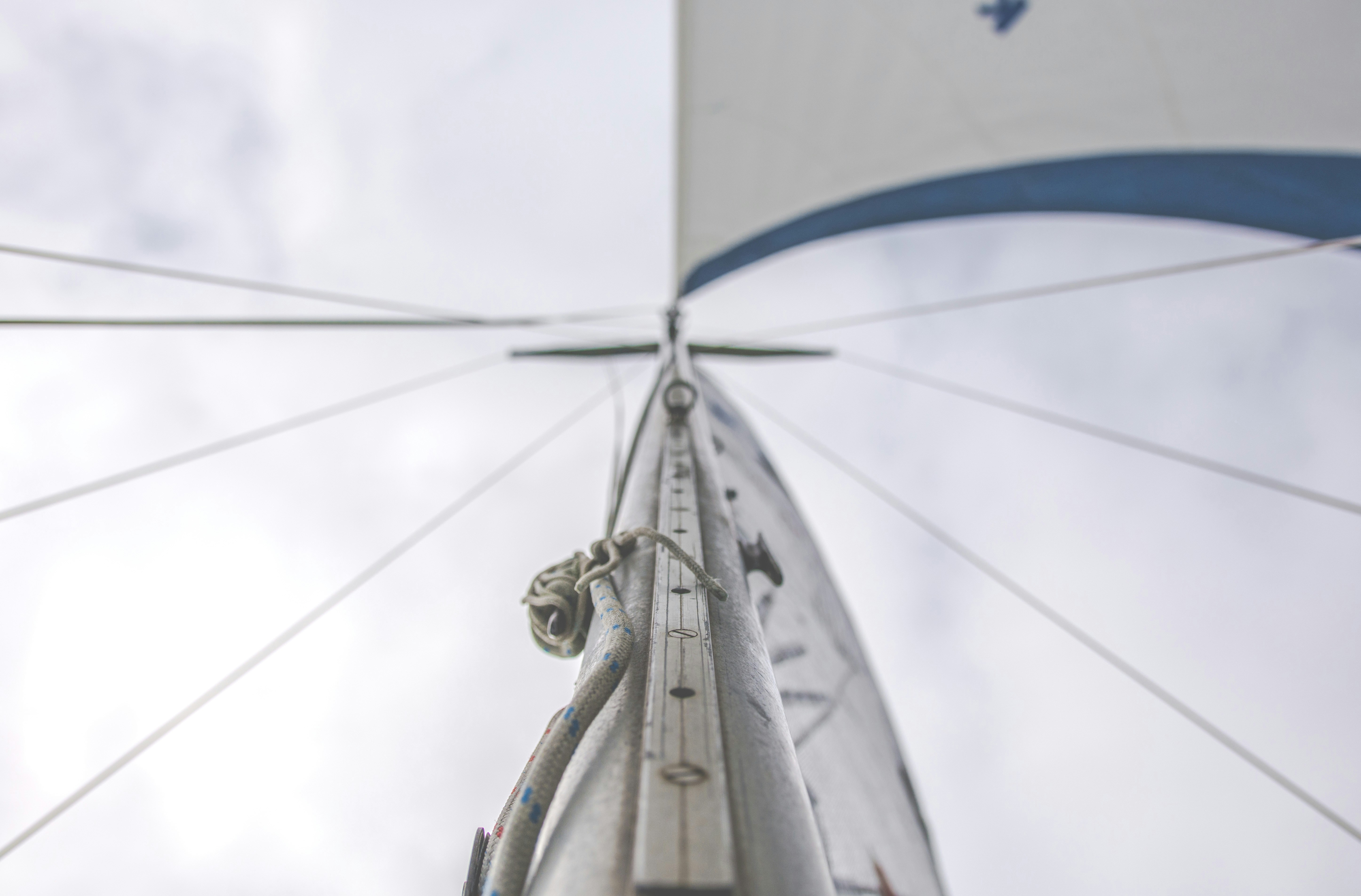 Looking up at a yacht's mast and sails against a cloudy sky.