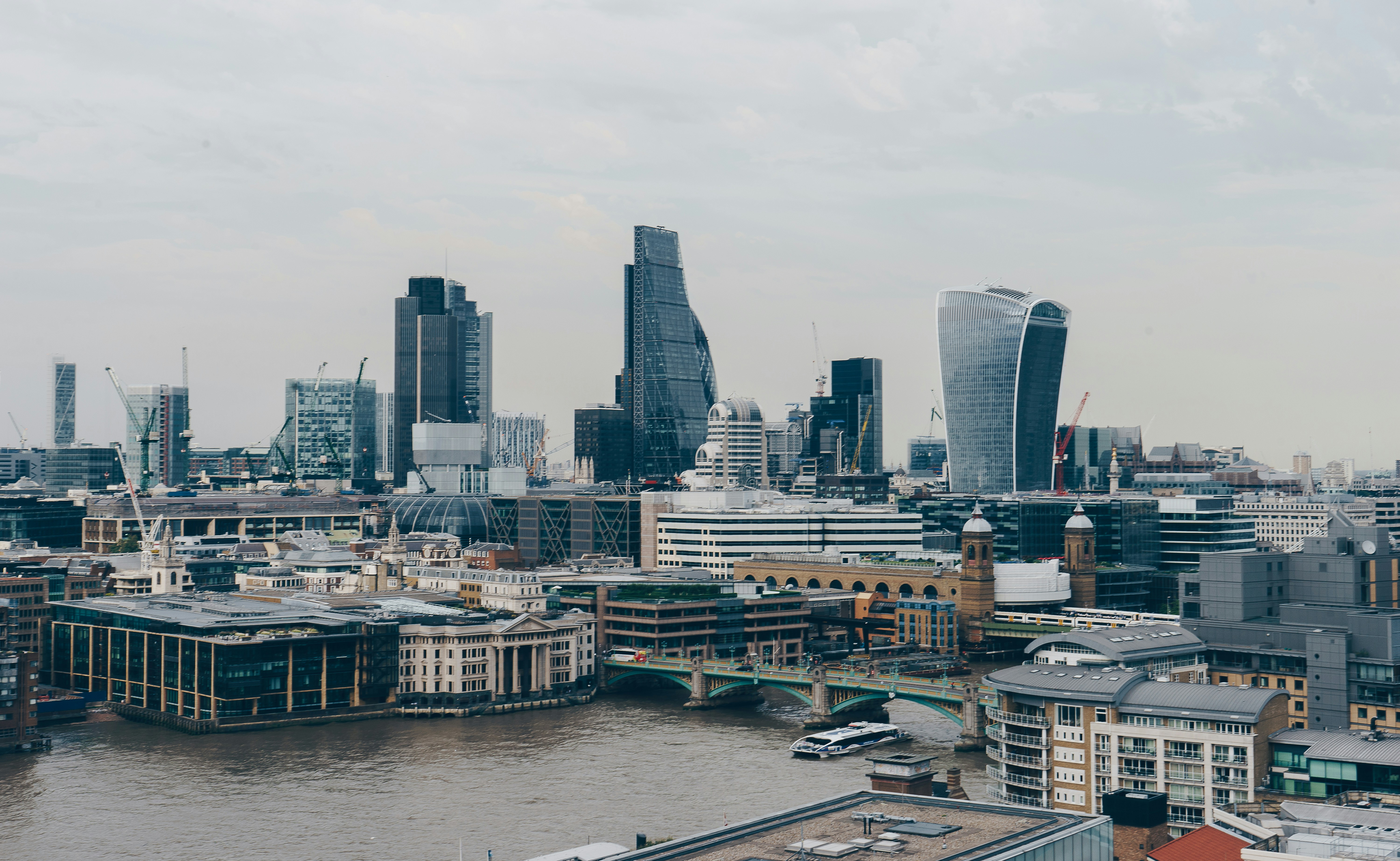 London skyline with modern skyscrapers and the Thames under a cloudy sky.
