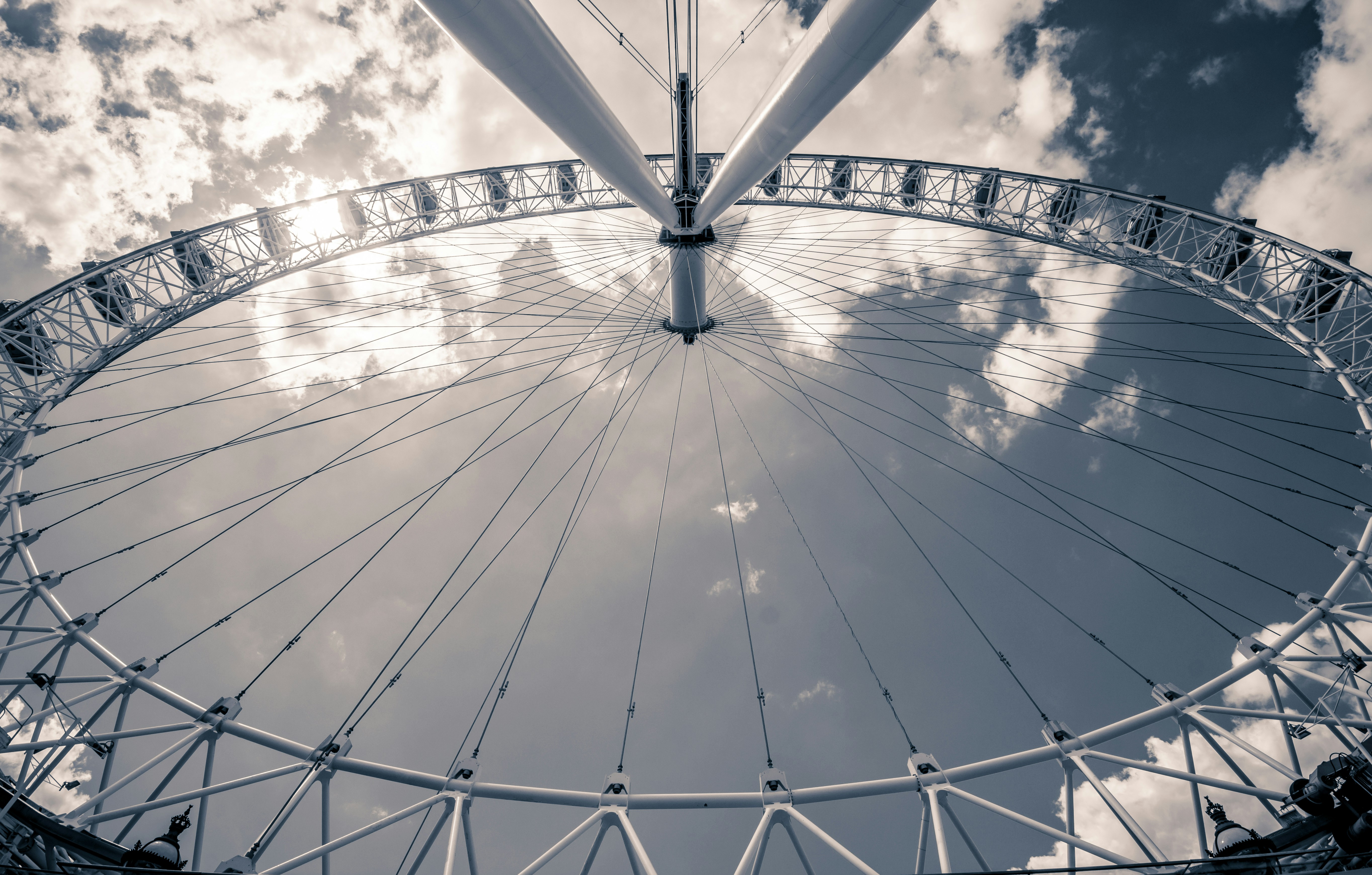 Looking up at the intricate structure of a giant Ferris wheel against a backdrop of clouds and sky.