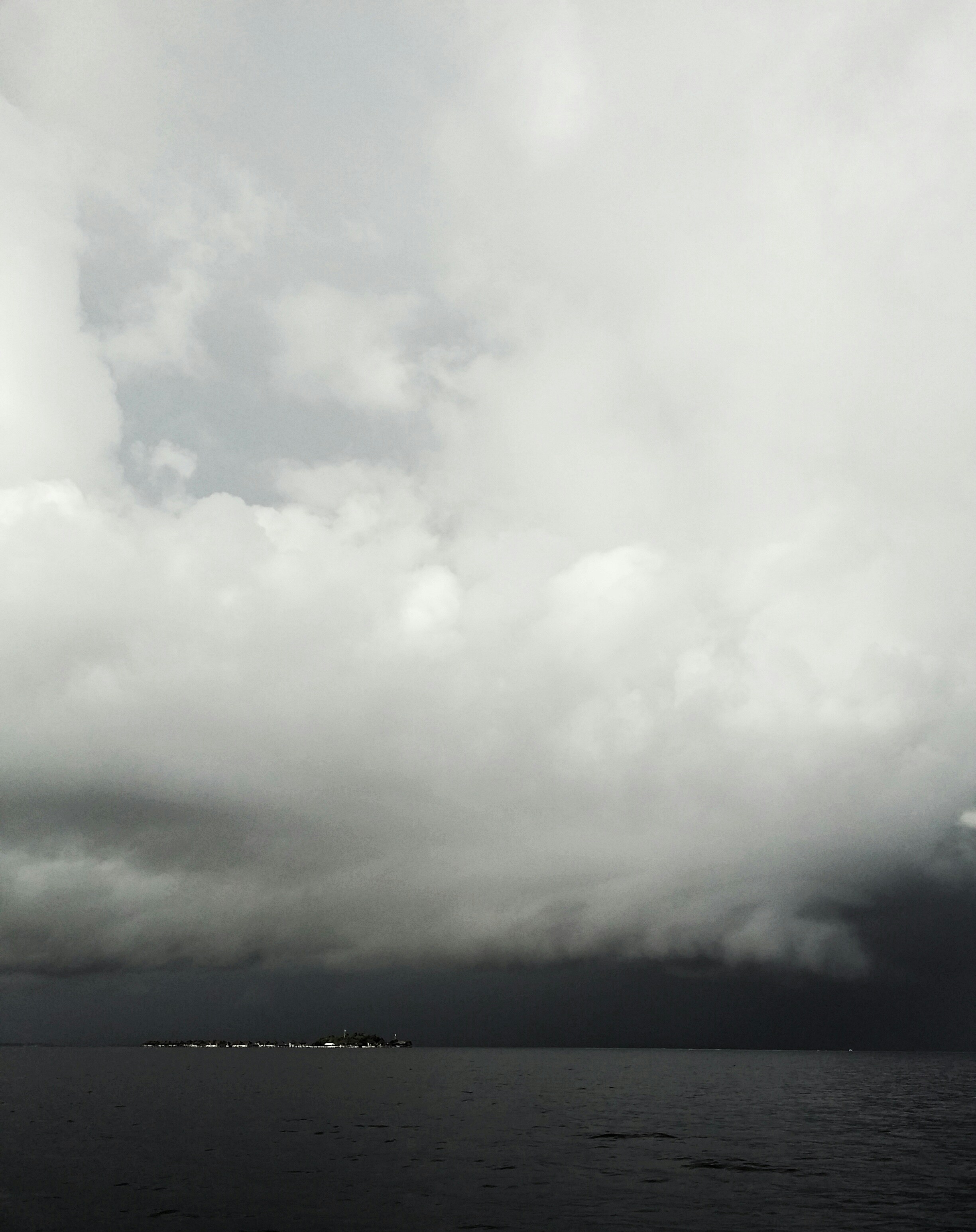 Dark clouds loom over a tranquil sea, hinting at an impending storm. A distant island silhouette adds depth to the moody landscape.