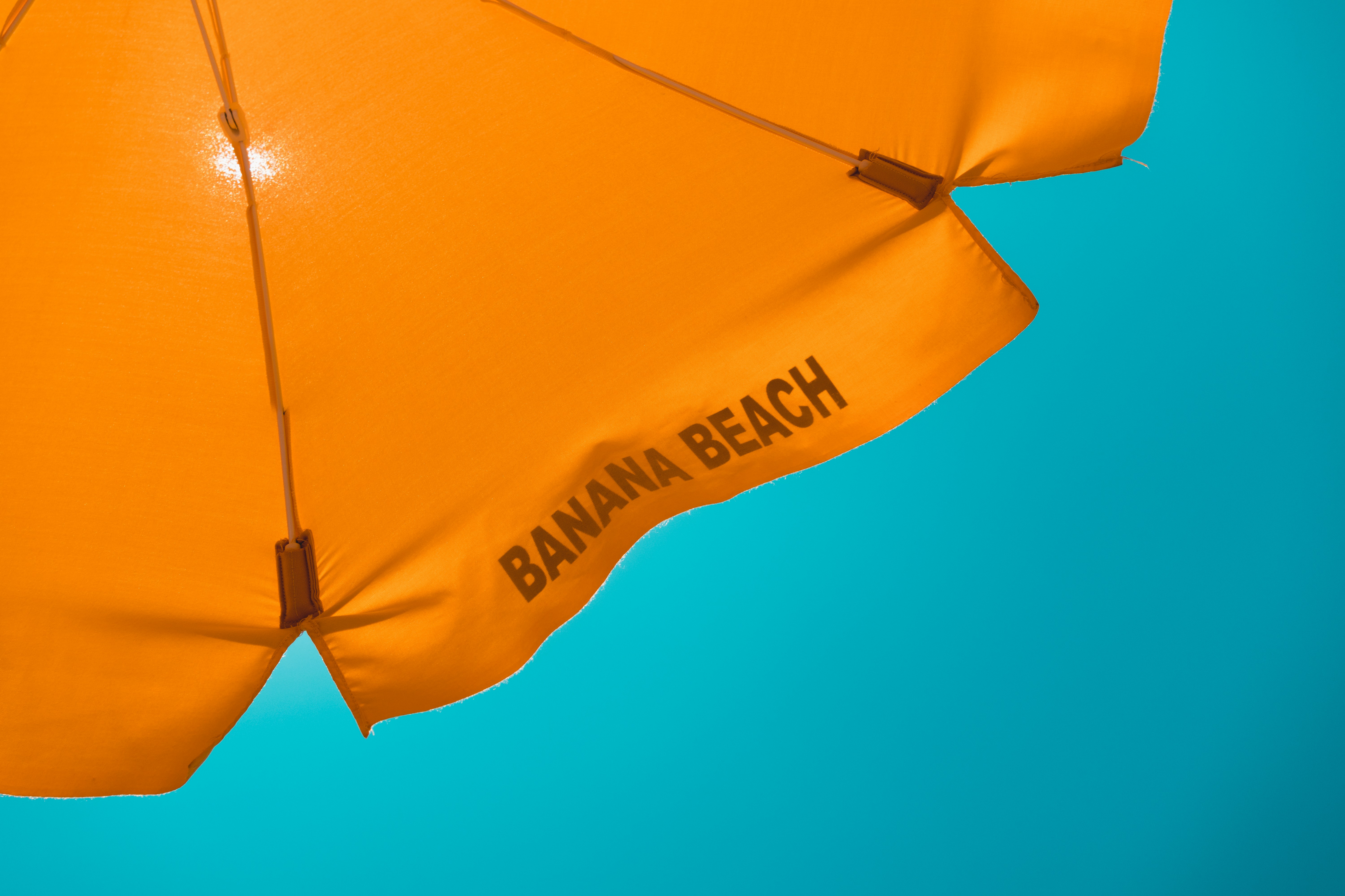Orange beach parasol with 'Banana Beach' text against a clear blue sky.