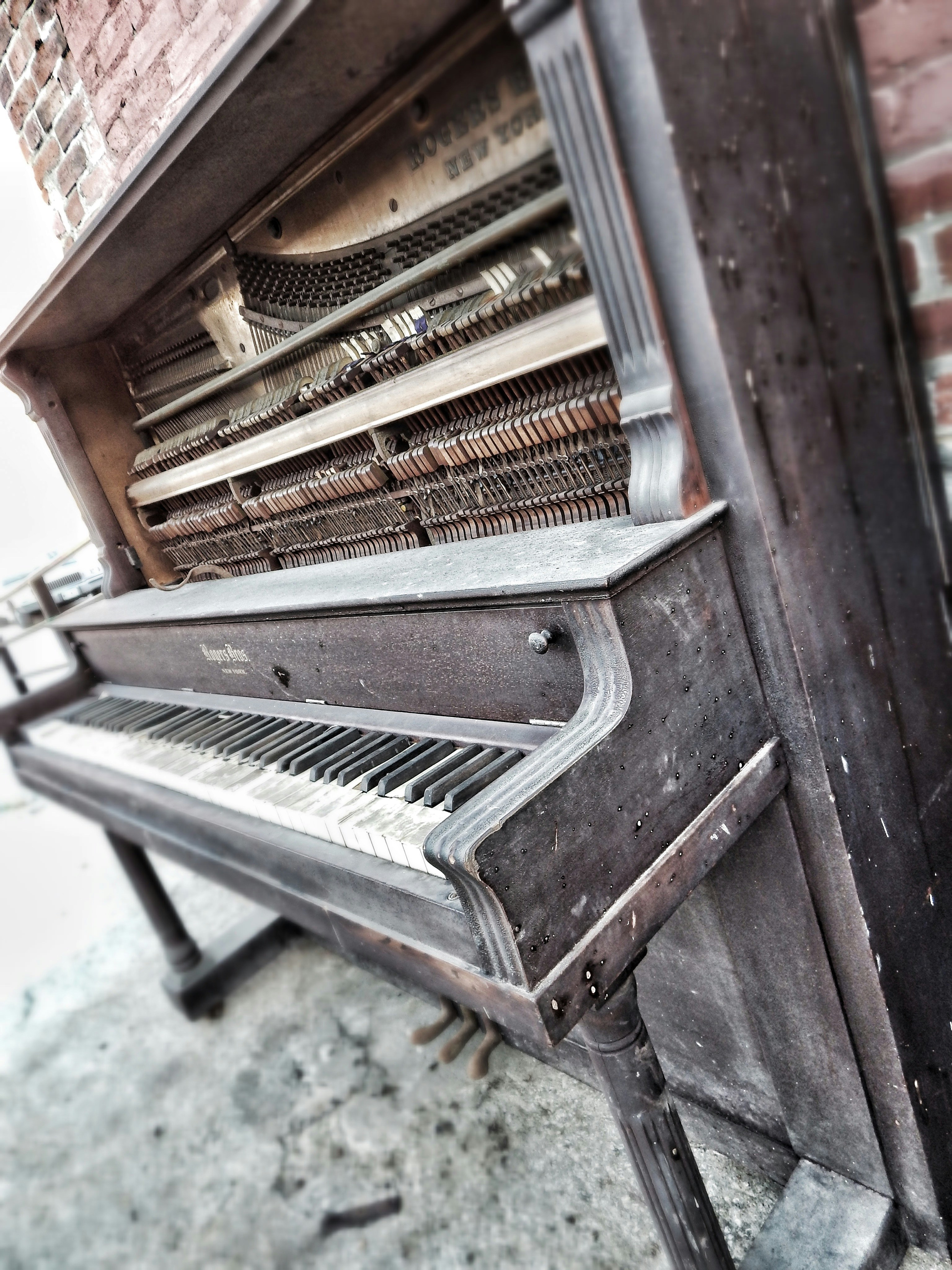 An antique piano stands against a brick wall, showcasing its intricate inner workings and aged keys. The weathered exterior hints at a rich history of music and memories.