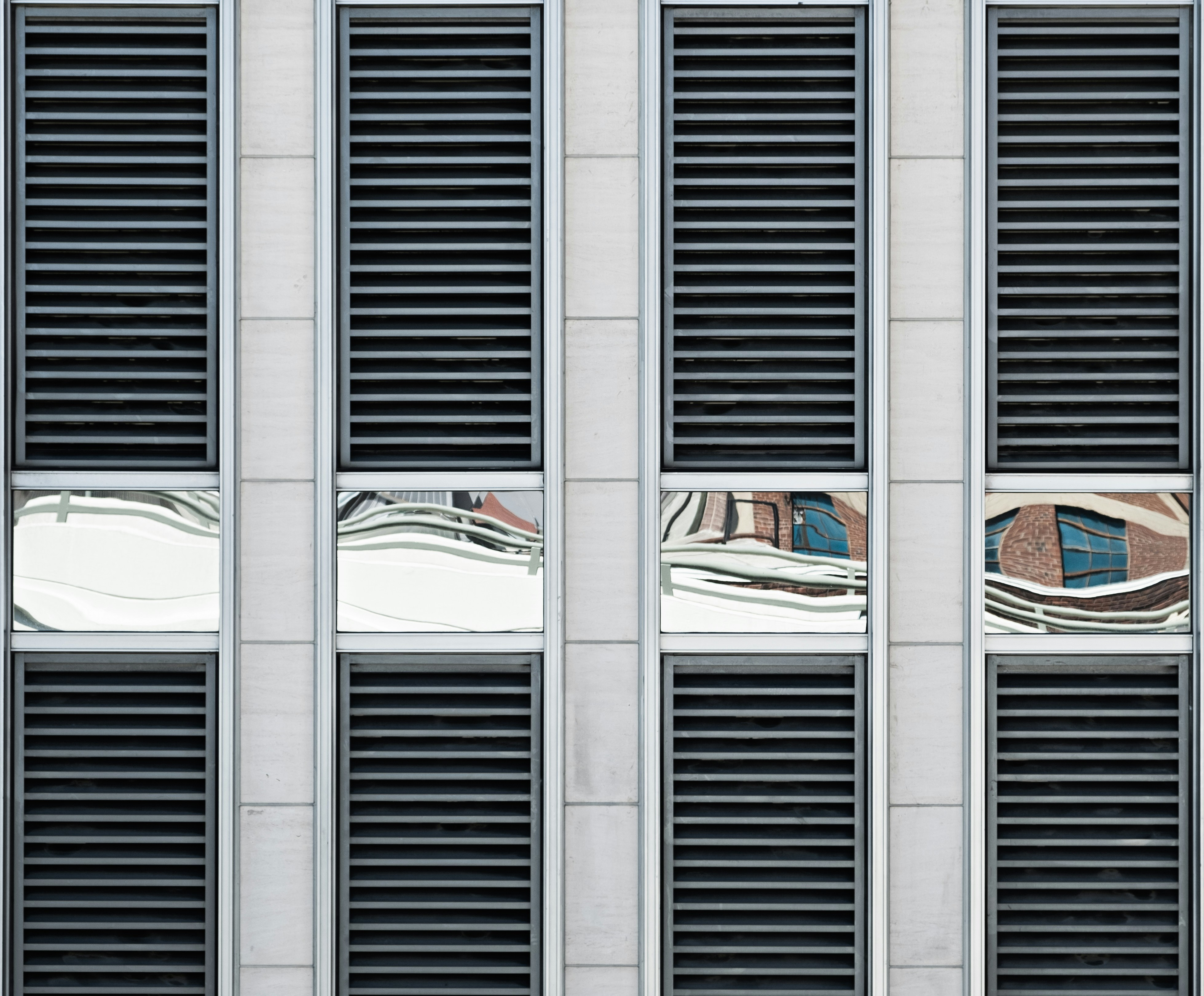 Symmetrical facade with reflective windows distorting urban landscape.