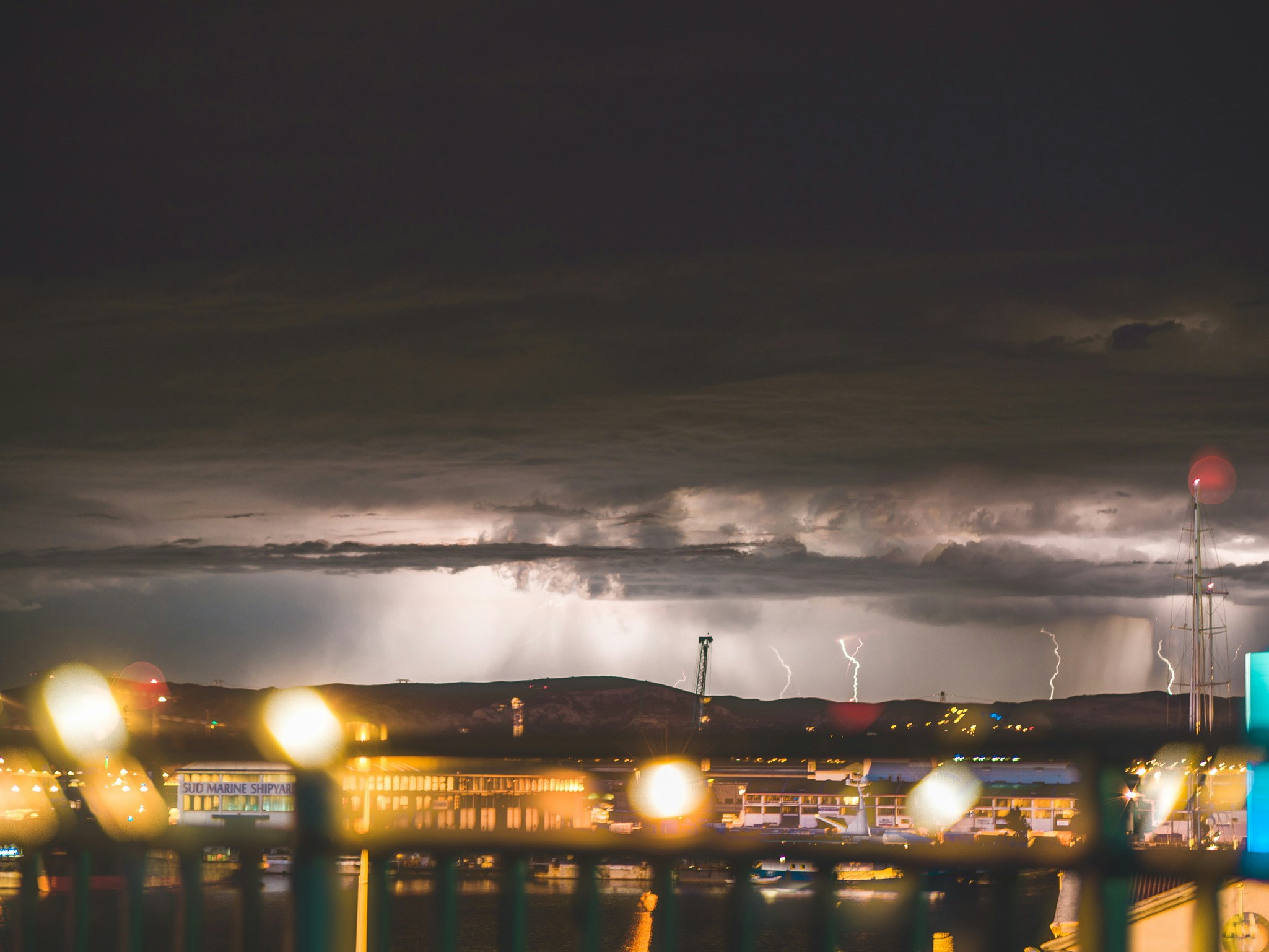 Dramatic lightning illuminating a stormy sky over a cityscape, with blurred city lights in the foreground.