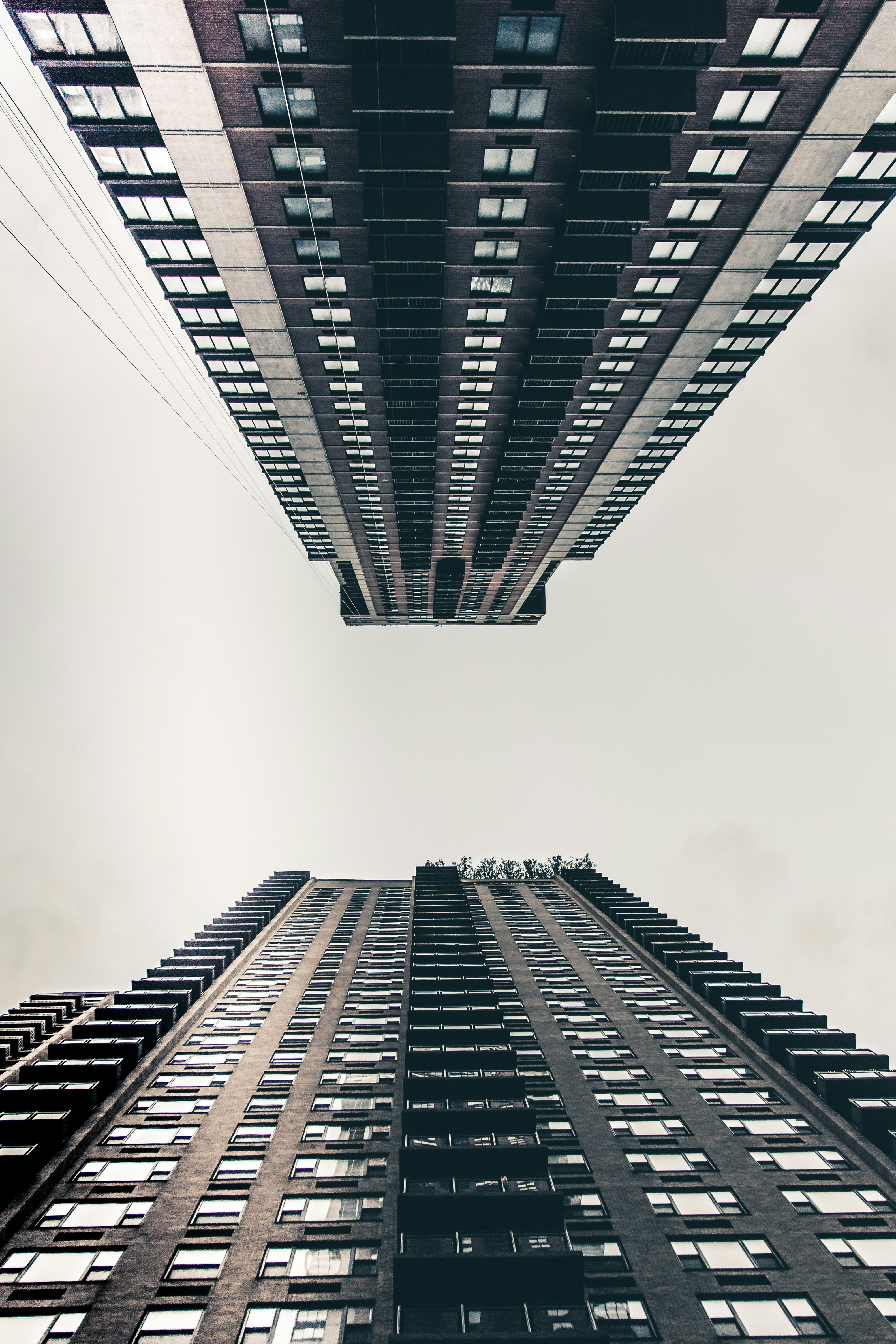 Worm's eye view of two towering high-rise buildings converging against a pale sky.