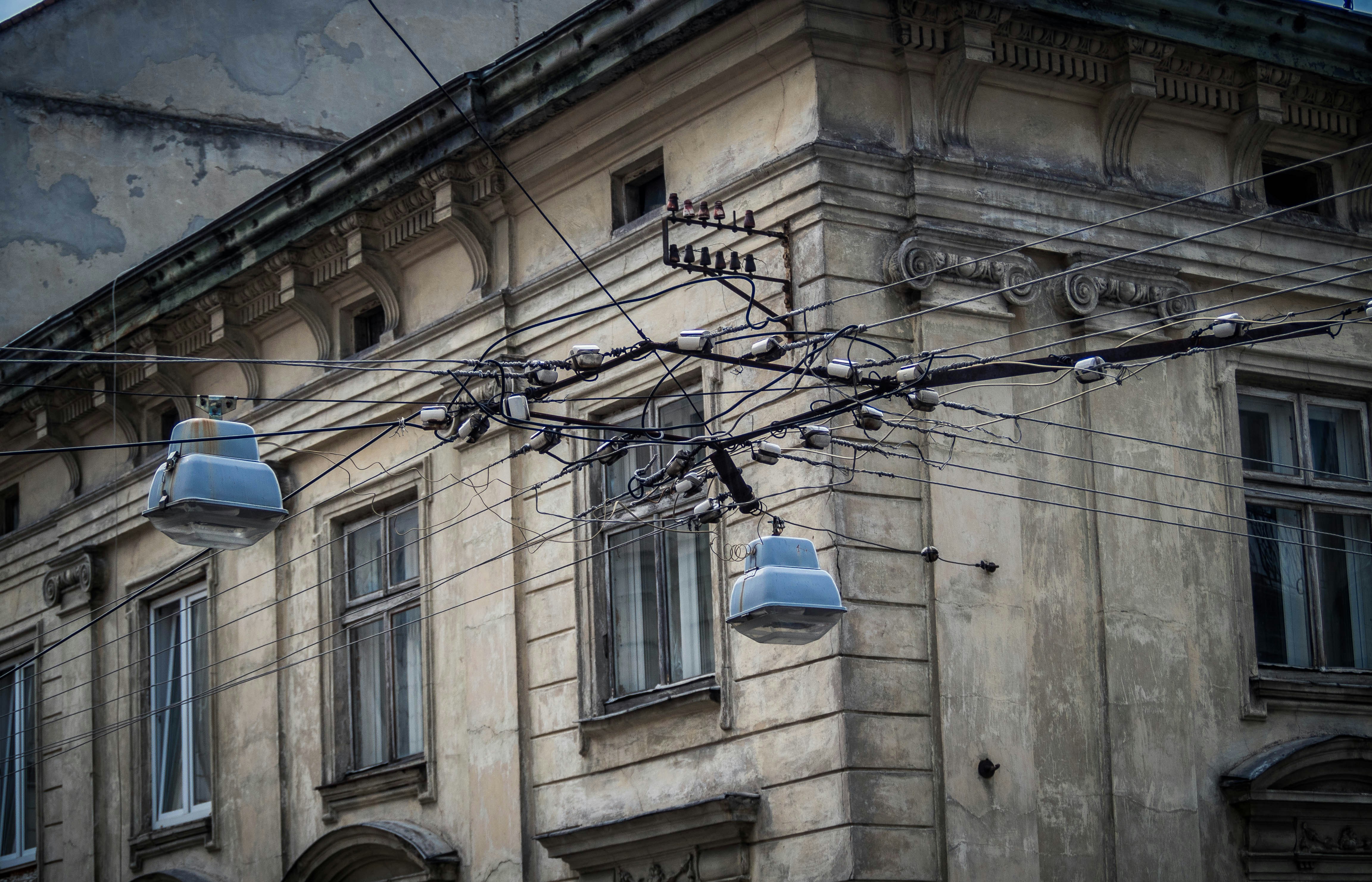 Old building facade adorned with intricate architectural details, intersected by overhead wires and streetlights.