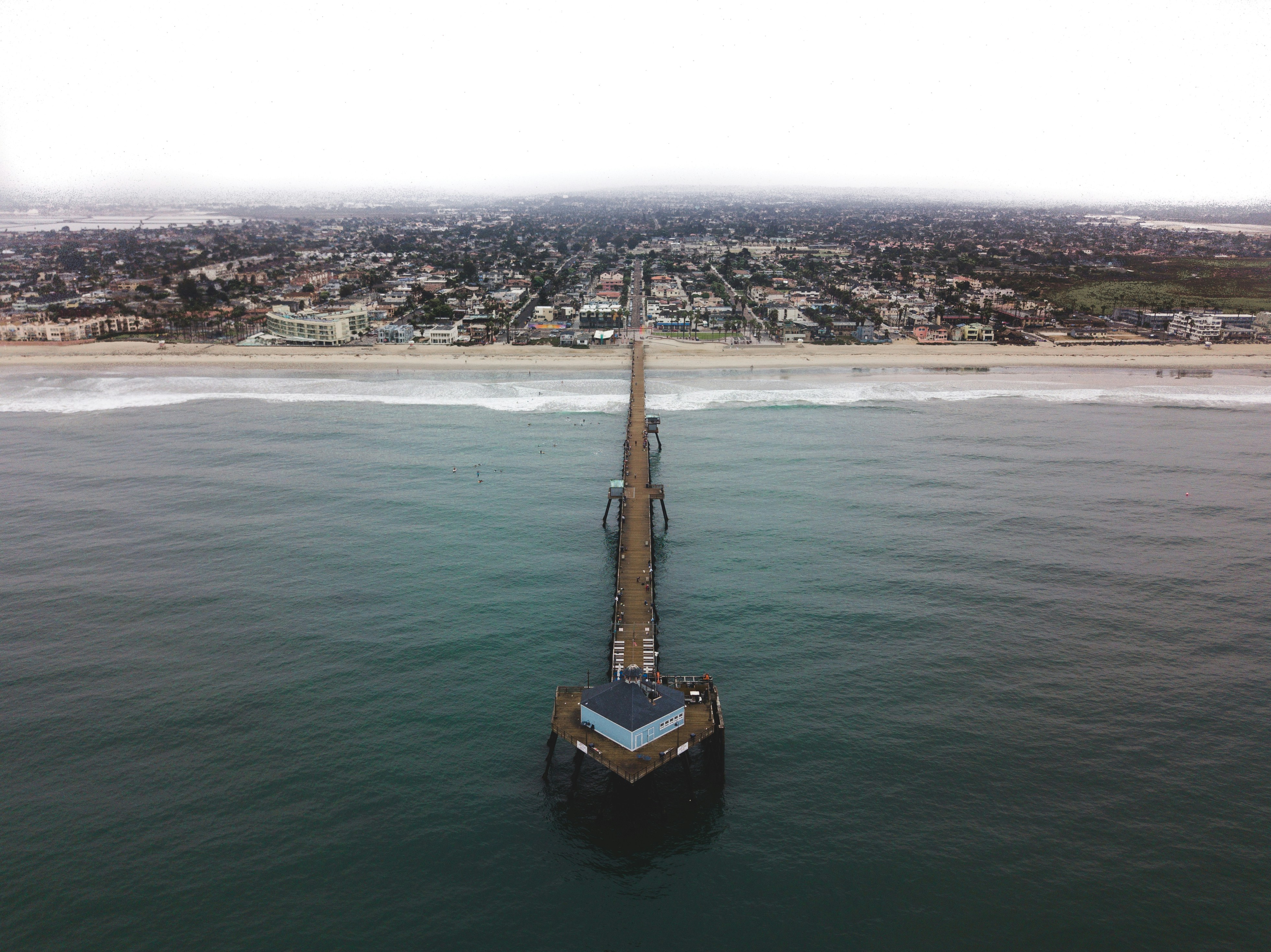 Long pier stretching into the ocean with a coastal town in the background under an overcast sky.