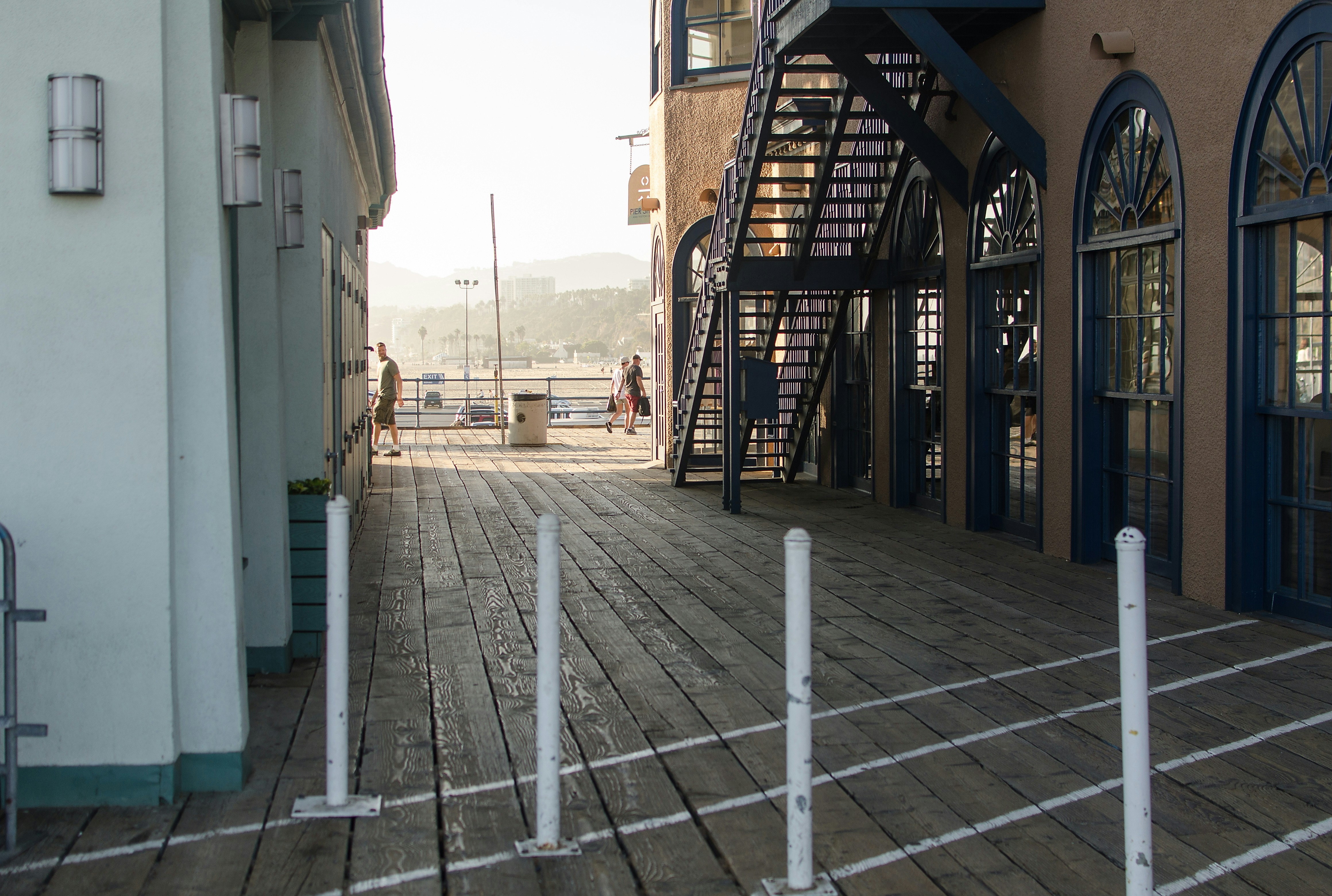 A serene boardwalk scene featuring a blend of architectural elements, with stairs leading to an upper level and distant figures enjoying the seaside atmosphere.