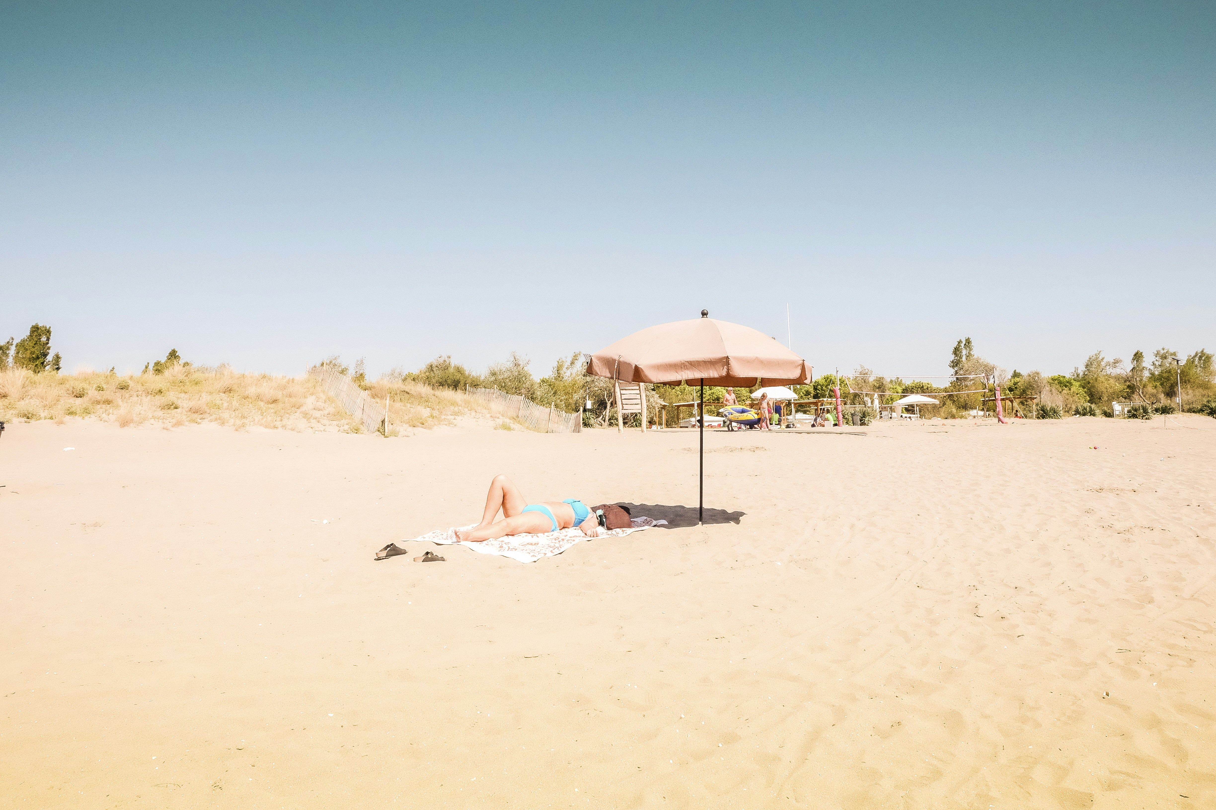 Single beach umbrella standing on a vast sandy shoreline under a clear blue sky.
