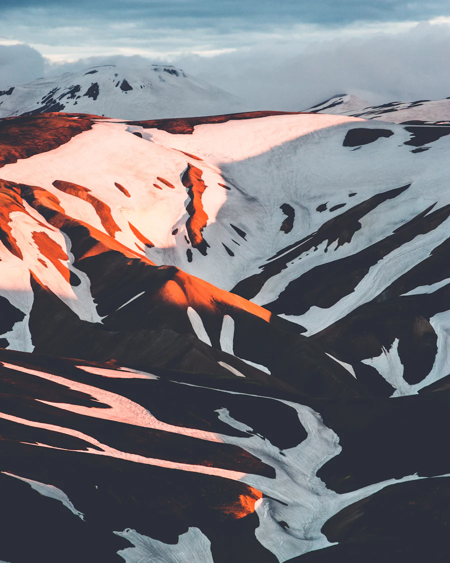 Snow-covered volcanic ridges lit by warm low-angle sunlight, with dark lava bands cutting through the landscape under a cloudy sky.