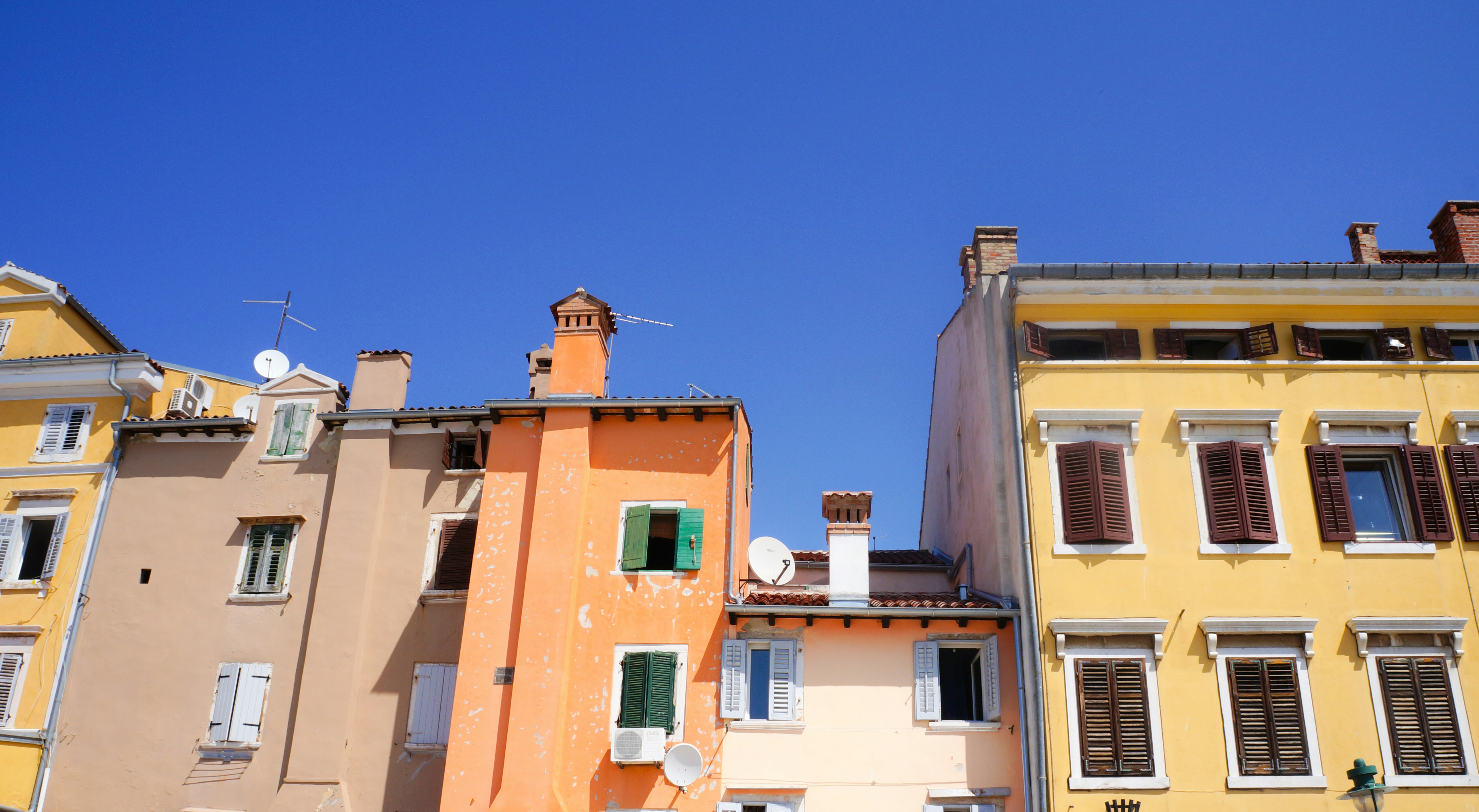 Yellow and orange buildings with wooden shutters beneath a bright blue sky.