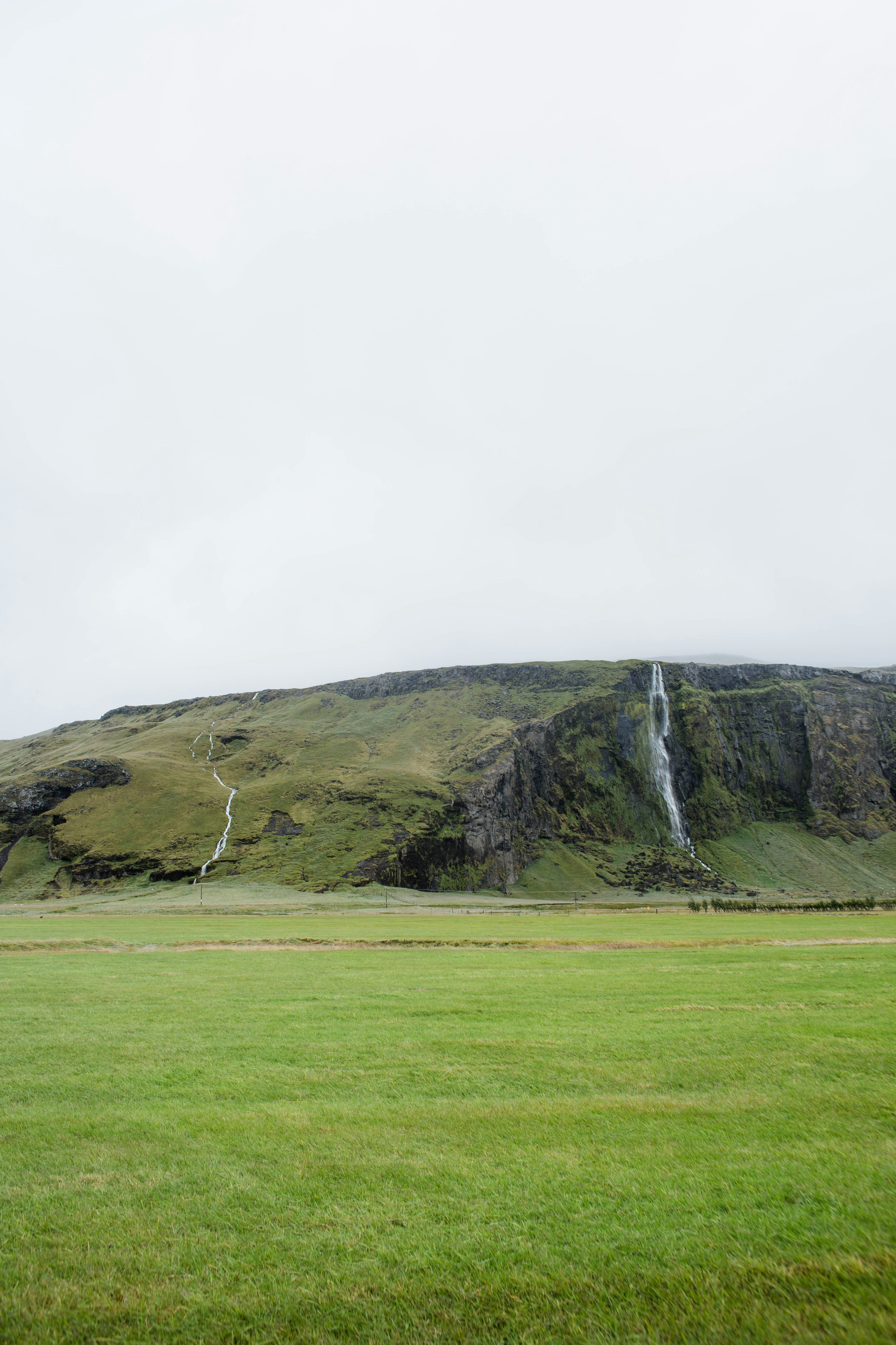 A lush hillside adorned with cascading waterfalls under a cloudy sky, showcasing the serene beauty of Icelandic landscapes.