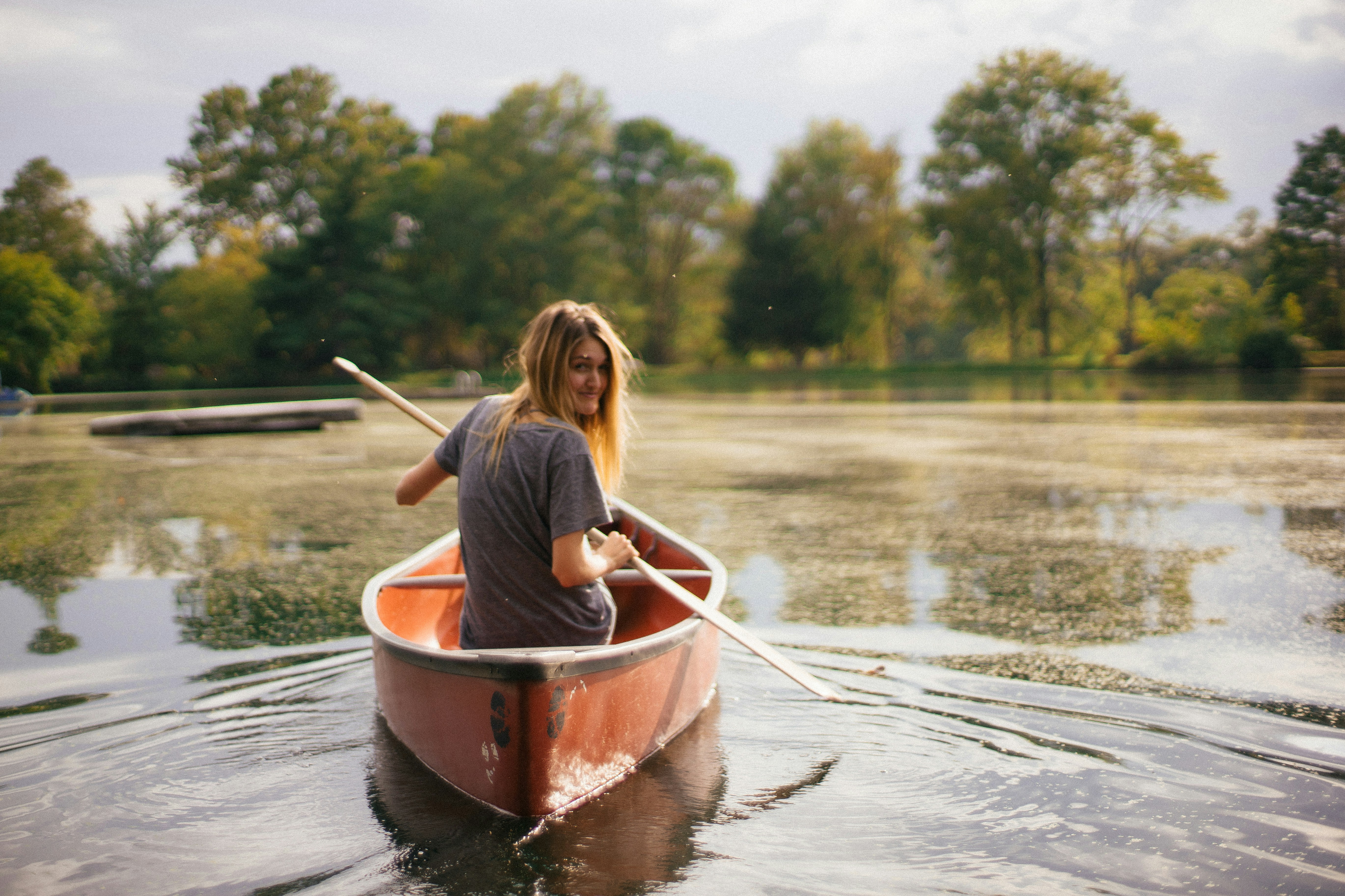 A woman paddling a canoe through a calm lake surrounded by lush greenery, capturing a moment of tranquility in nature.