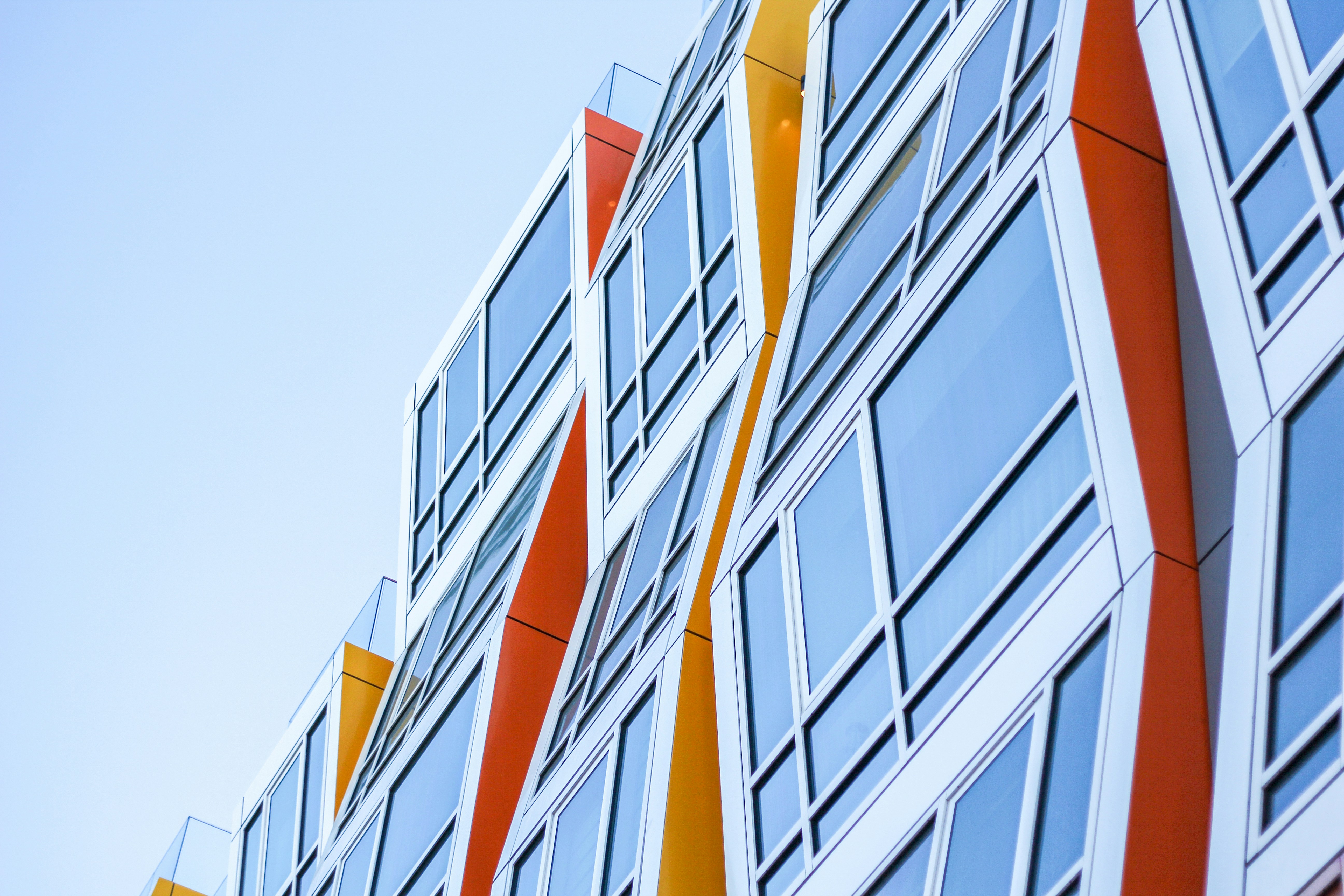 Modern building facade showcasing a dynamic arrangement of windows and vibrant orange accents against a clear sky.