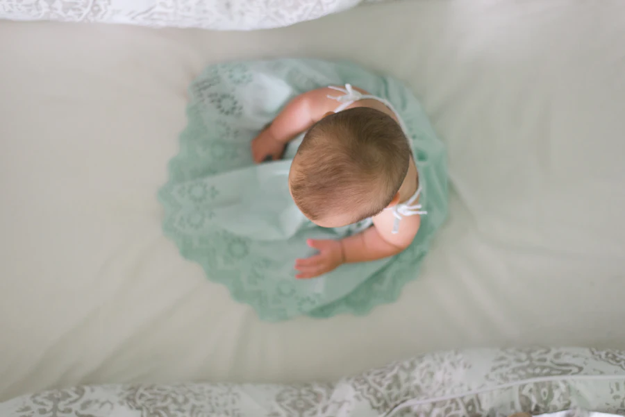 A young child in a delicate mint green dress sits on a soft surface, surrounded by white lace details. The scene conveys a sense of tranquility and innocence.